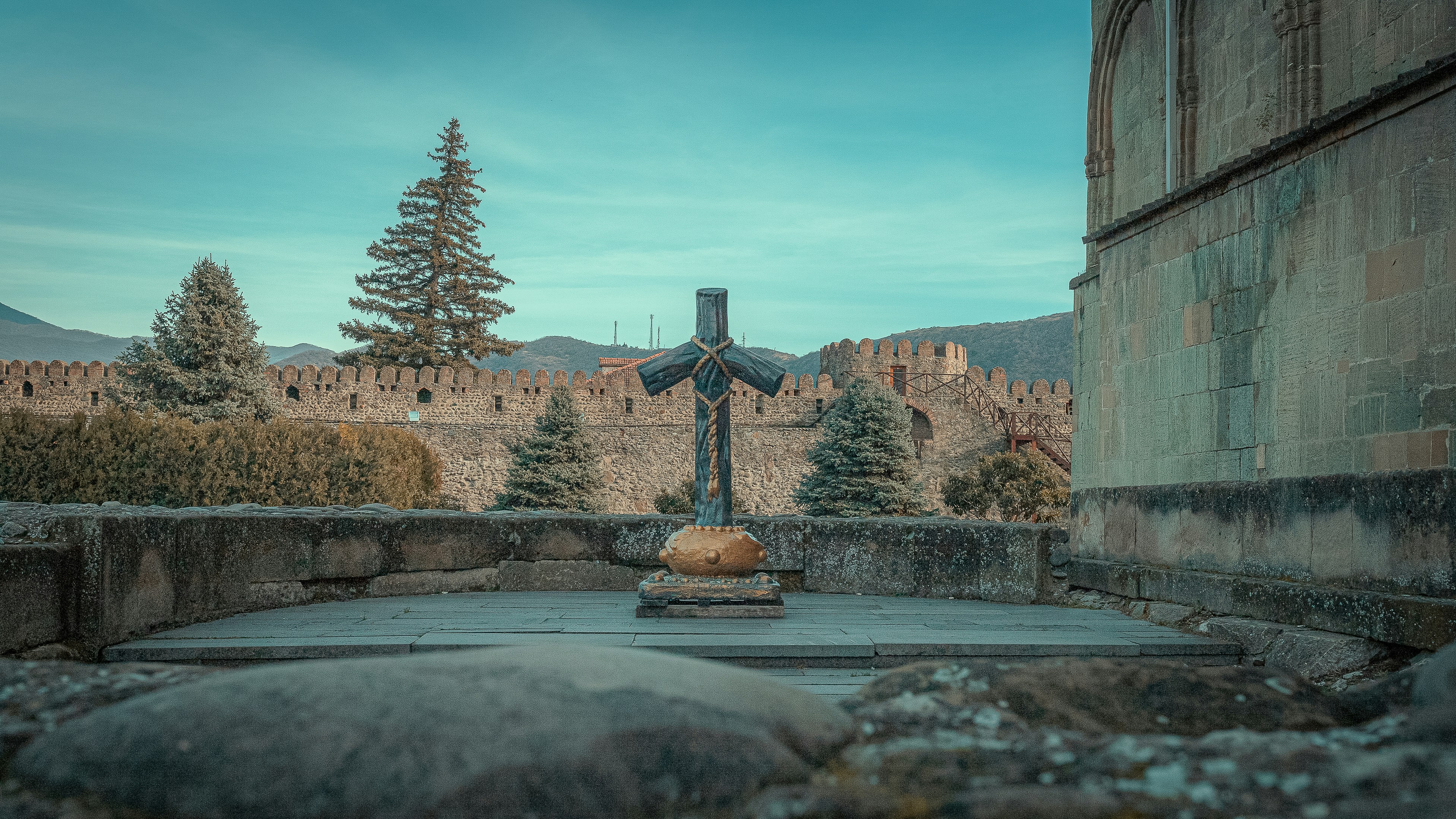 Cross on a Weathered Pedestal Framed by Castle Walls and Evergreen Silhouettes