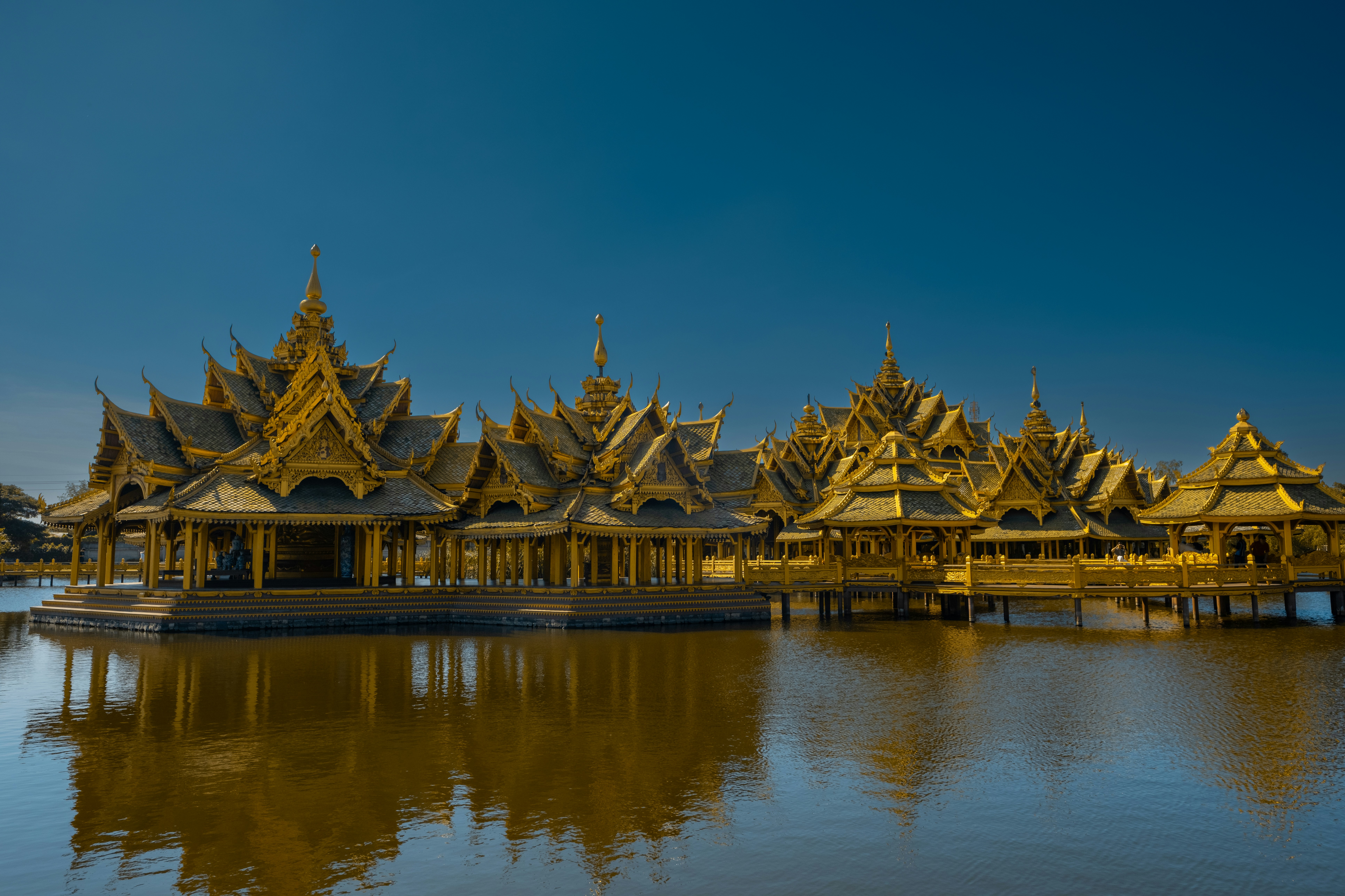 Traditional Thai architecture mirrored in calm waters under a clear blue sky.
