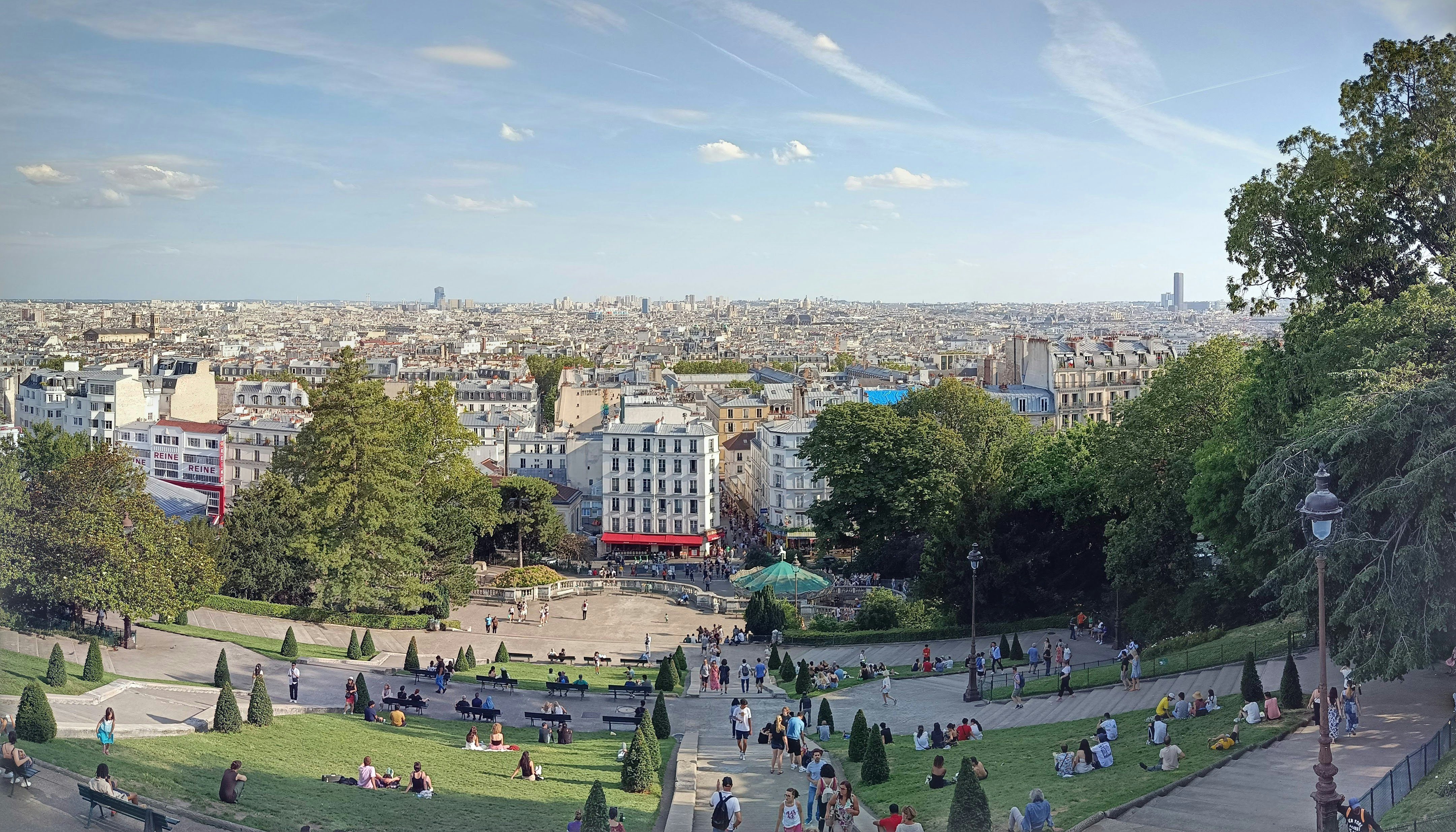 Expansive cityscape view with scattered trees and people on a hill under a clear sky.