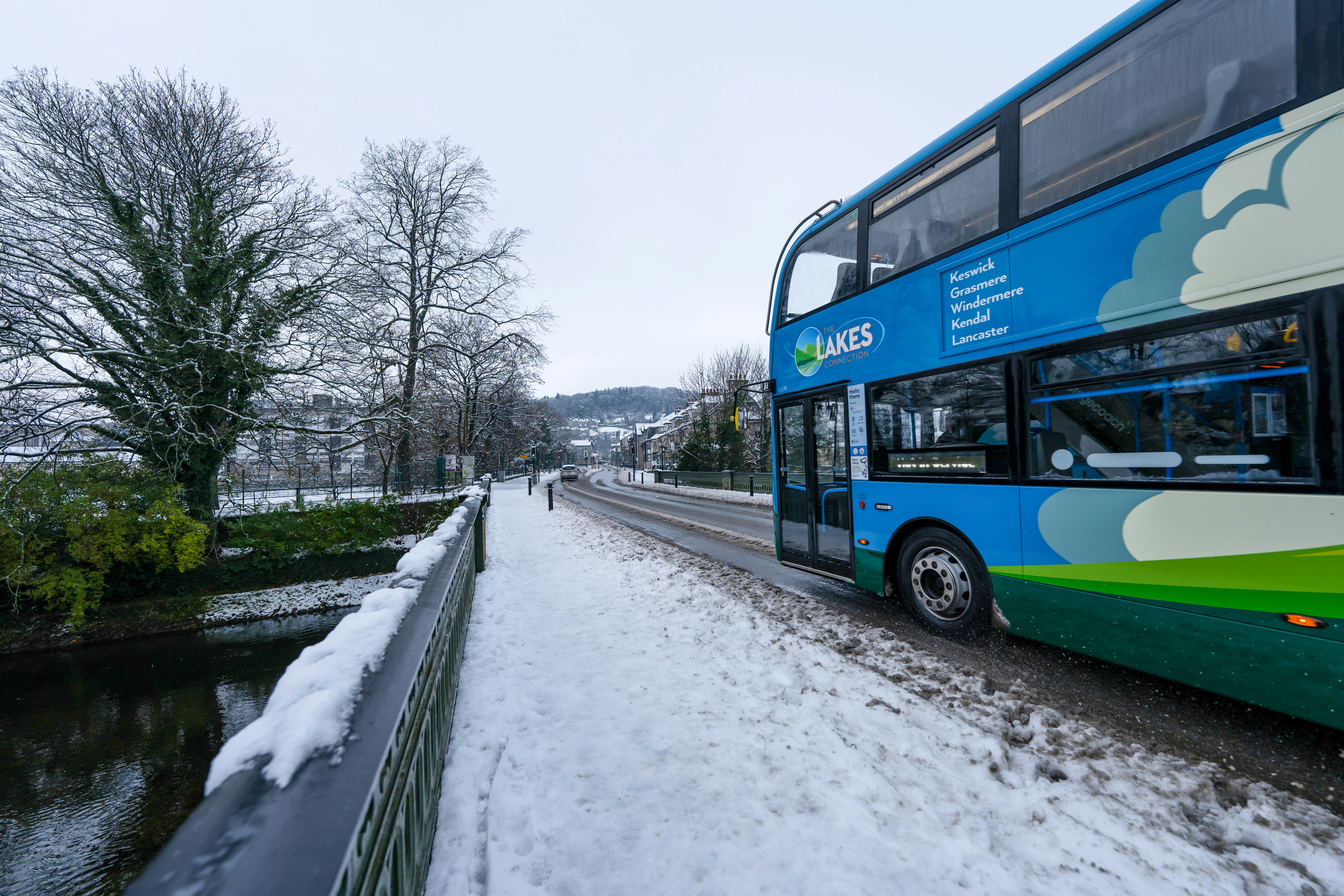 A blue double decker bus driving down a snow covered road photo – Free ...