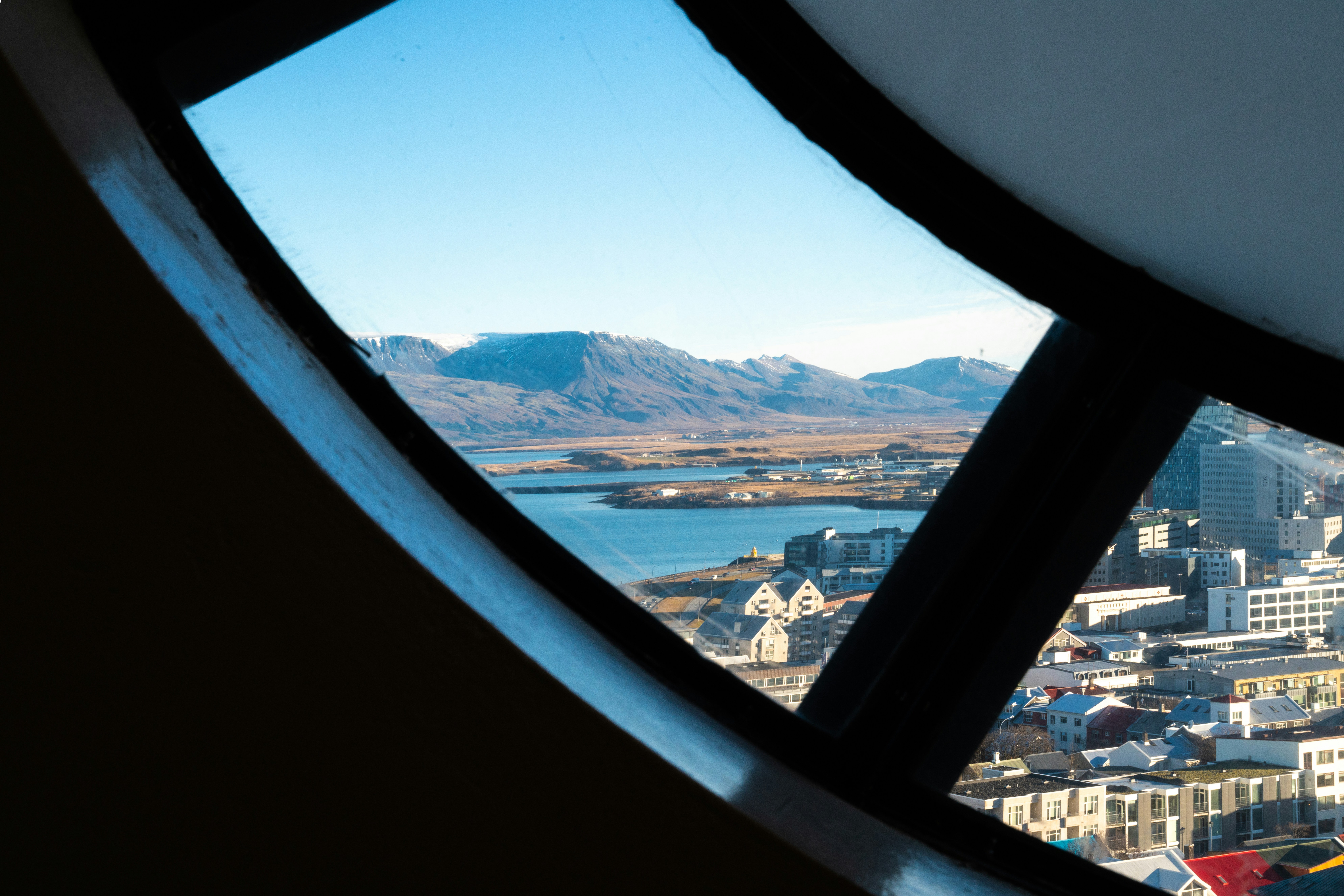 Through a Circular Window: Mountain Veil Over a Quiet Harbor