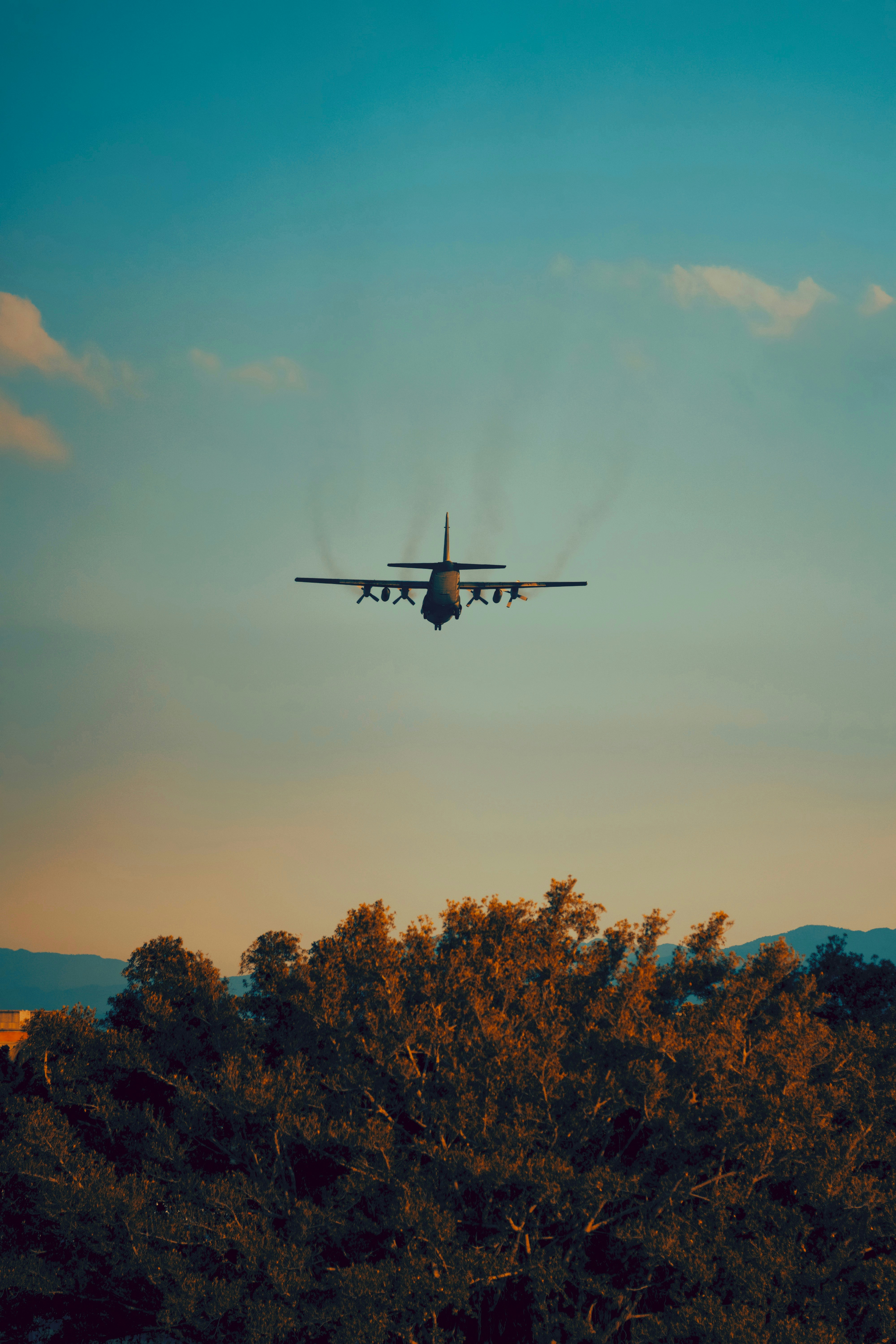 A large airplane flying over a forest under a blue sky photo – Free ...