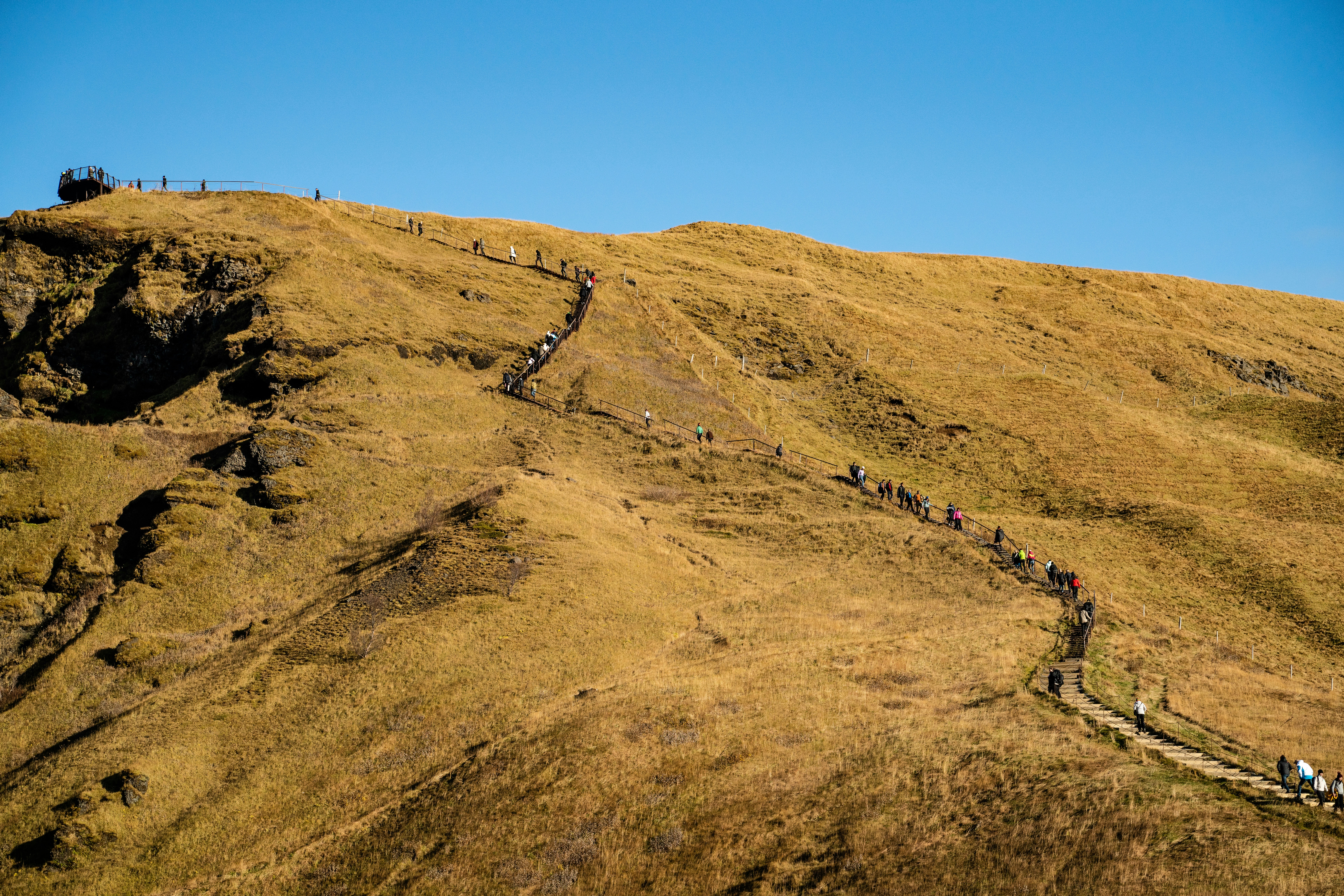 The Serpentine Ascent: Hikers Thread a Sunlit Hill