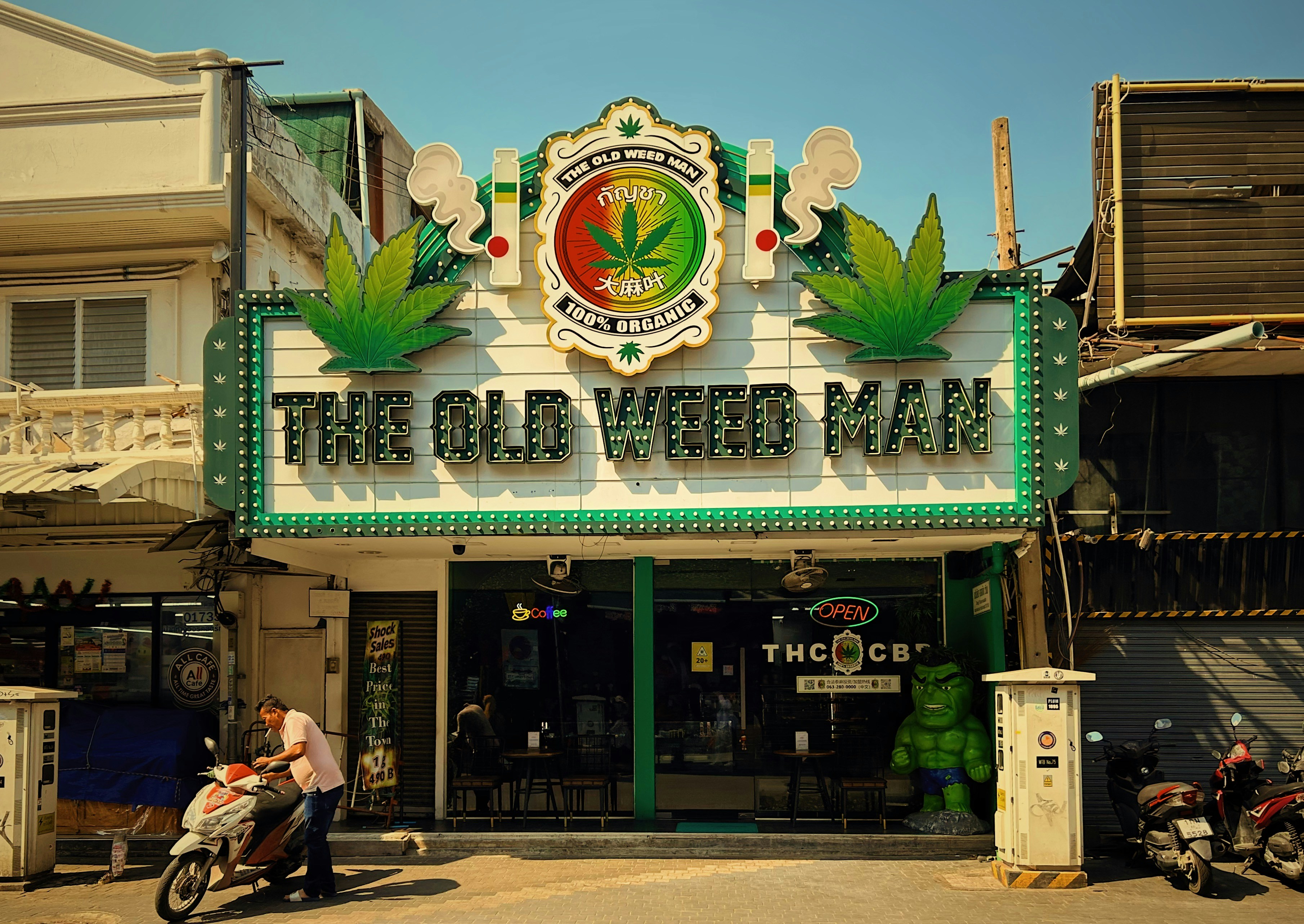 Vibrant storefront of The Old Weed Man, adorned with cannabis leaves and neon lights, inviting passersby to explore its offerings.