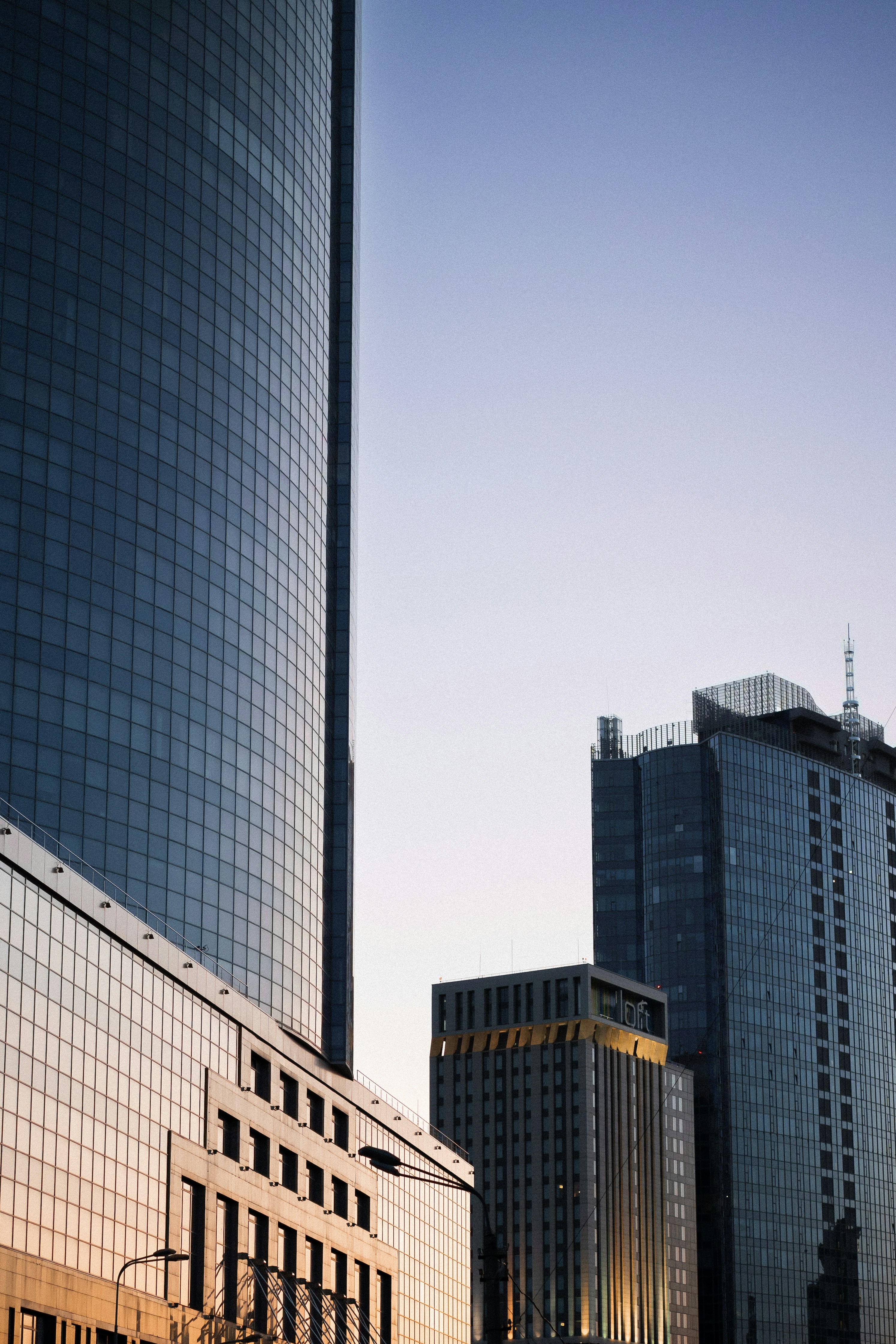 Modern skyscrapers reflecting the warm hues of a setting sun against a clear evening sky.