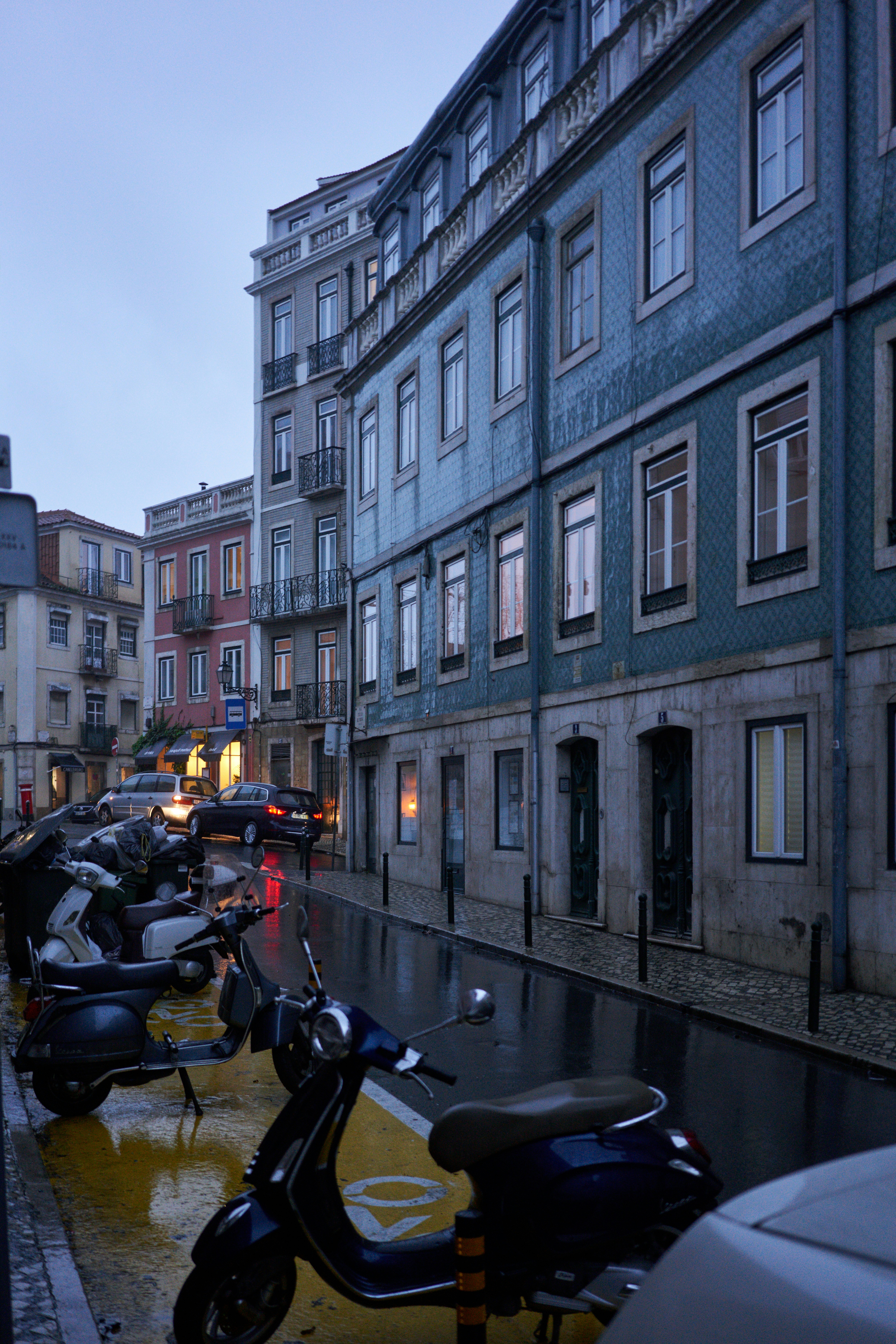 Blue-Tiled Dusk: Rain-Slick Street and Scooters by a Narrow European Lane