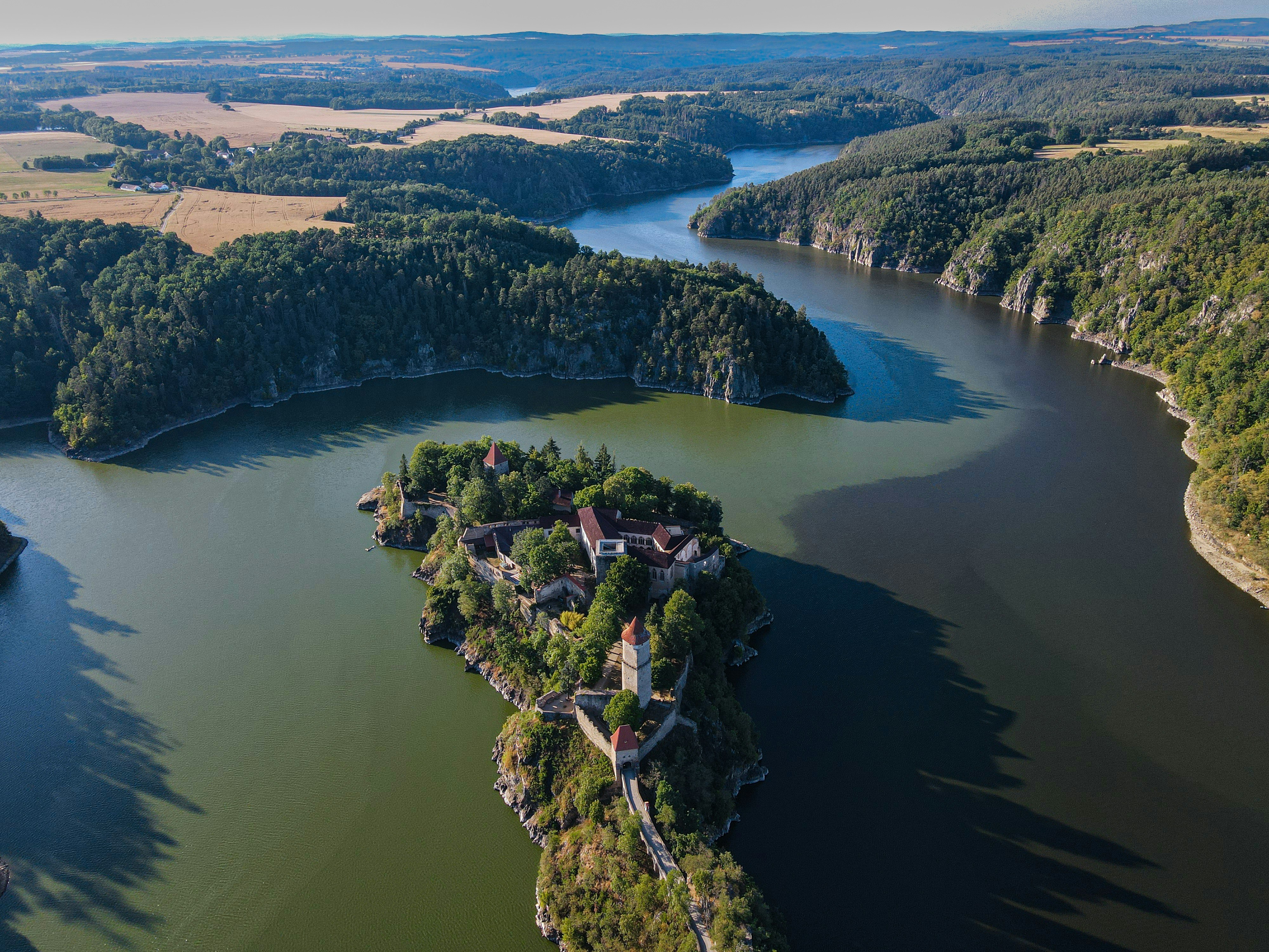 Aerial view of a winding river embracing a lush, forested island with a historical building at its center.