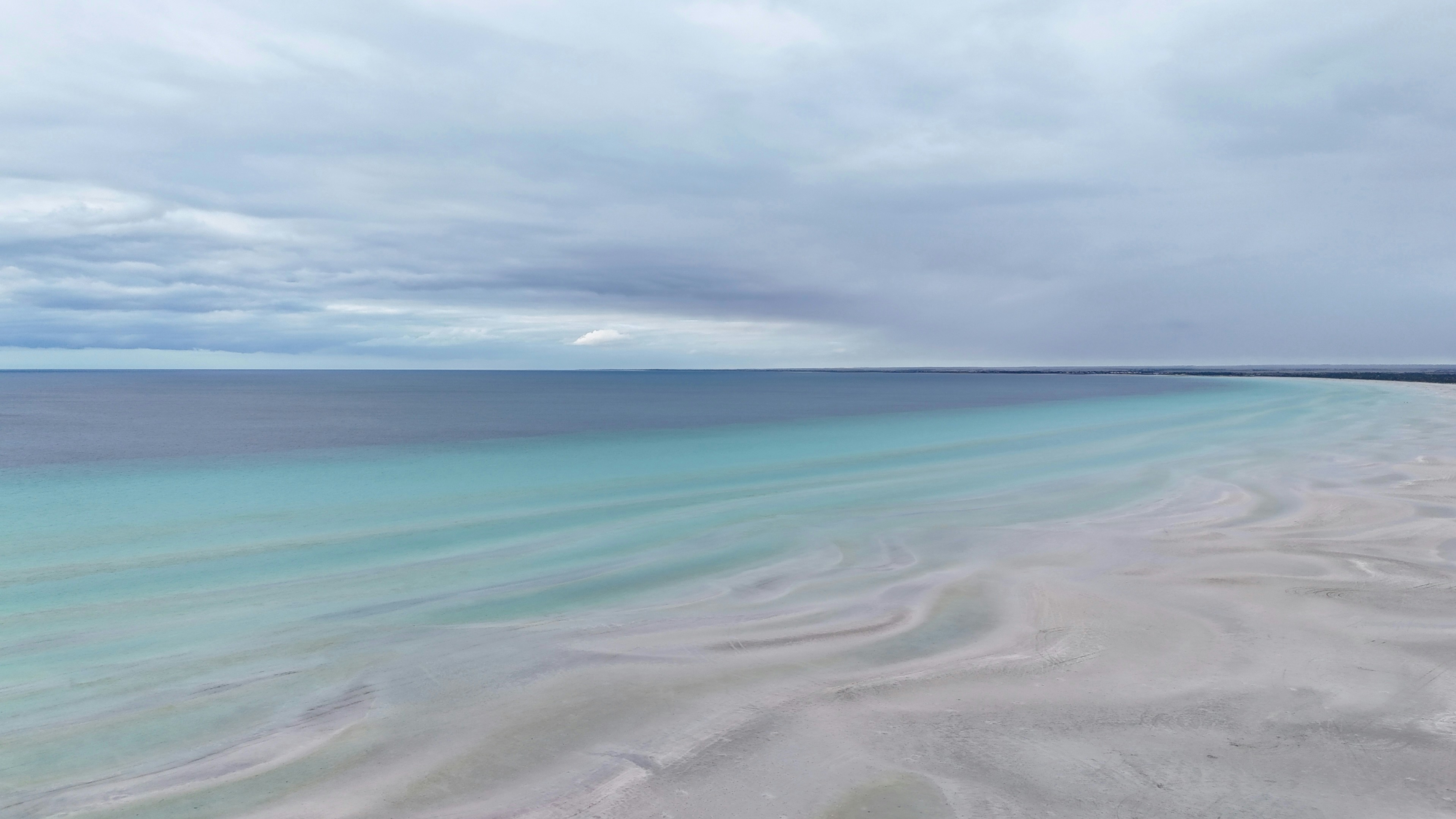 Turquoise Shoreline: Sand Ripples Meet a Cloudy Horizon