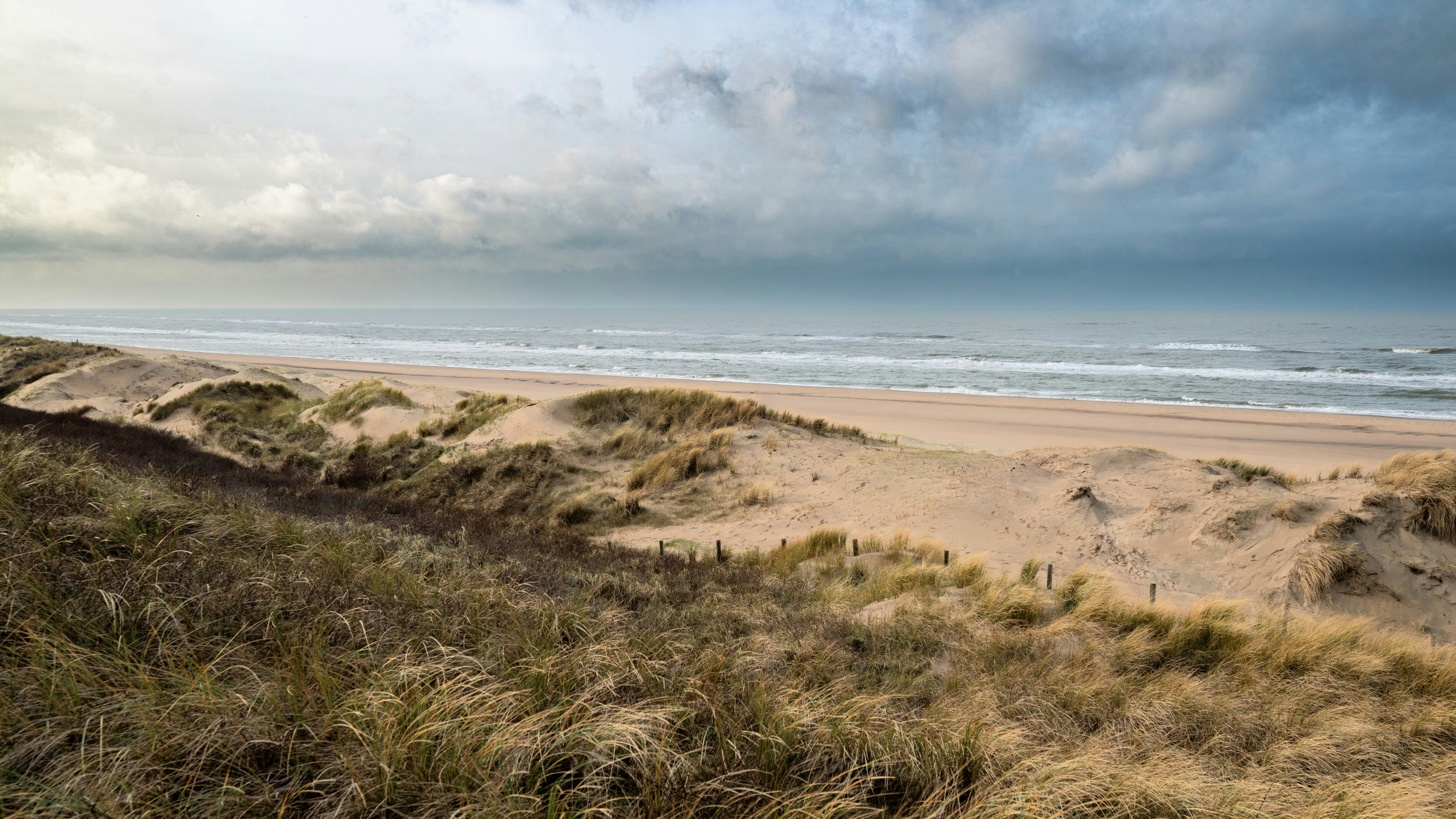 Sandy dunes stretch toward a distant shoreline beneath a cloudy sky.