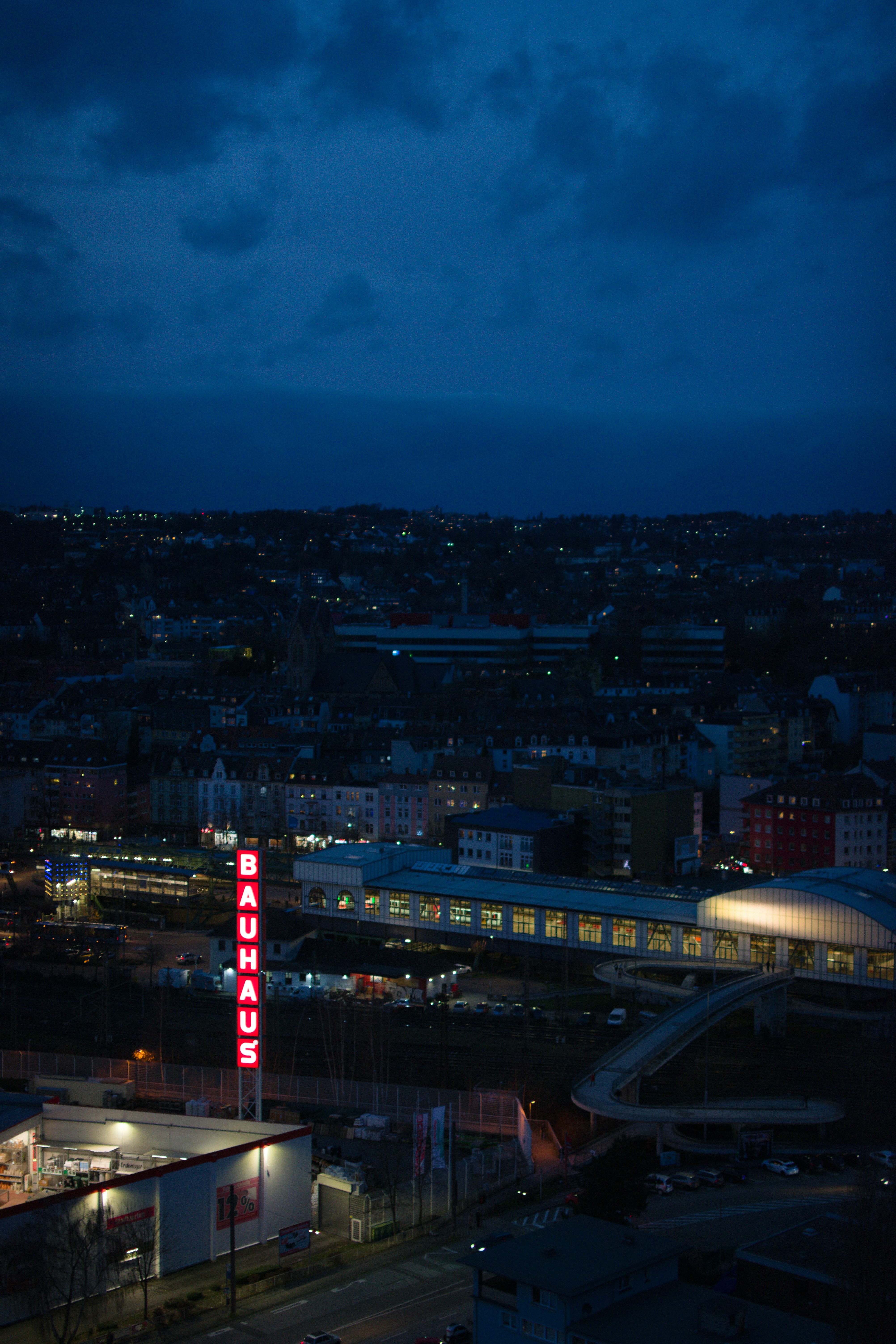Wuppertal cityscape at night featuring a suspension railroad and illuminated Bauhaus store.