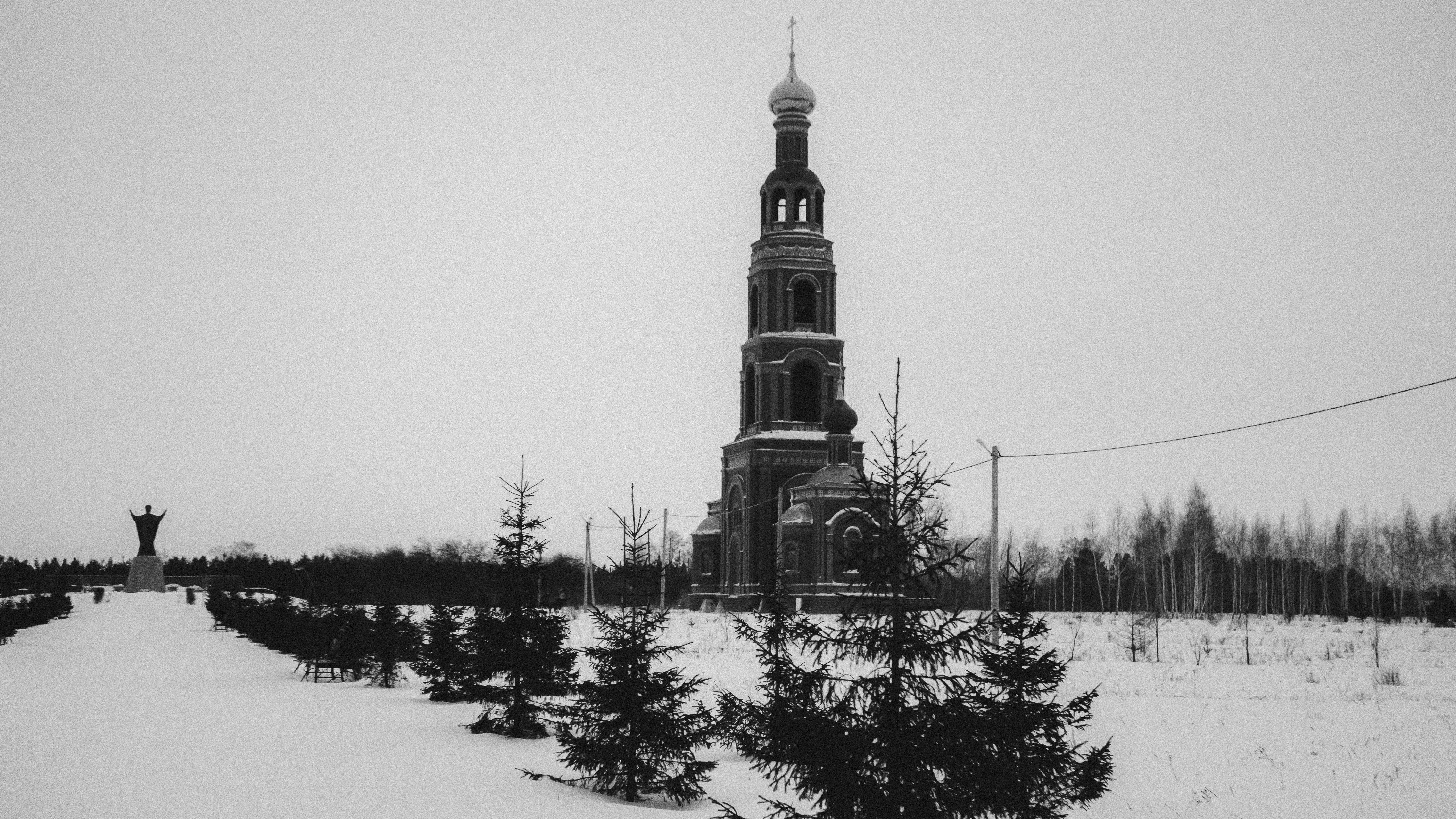 Snow-covered landscape with a tall, ornate tower rising against a stark winter sky.