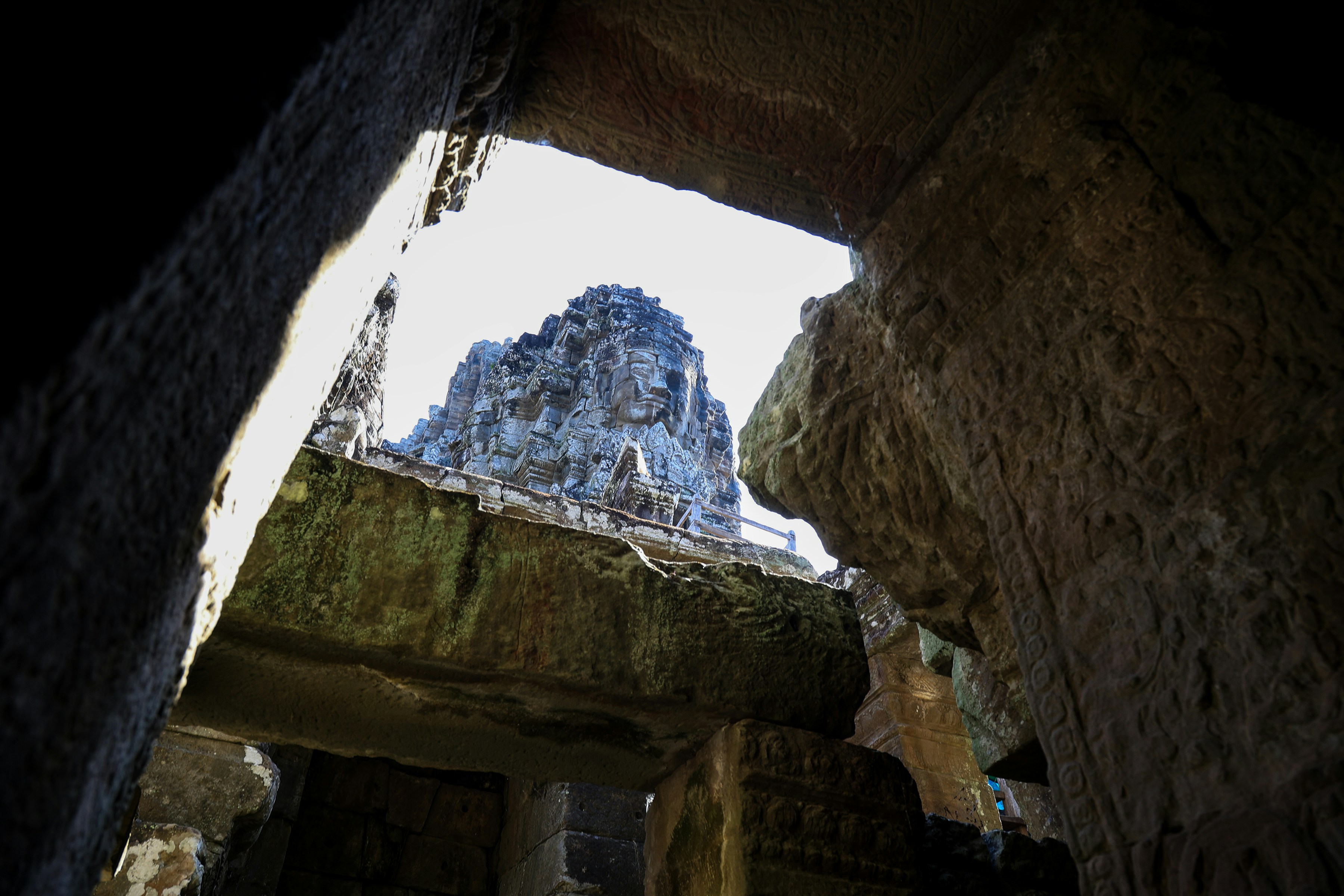 Intricate stone carvings of a temple face framed by ancient archways under bright daylight.