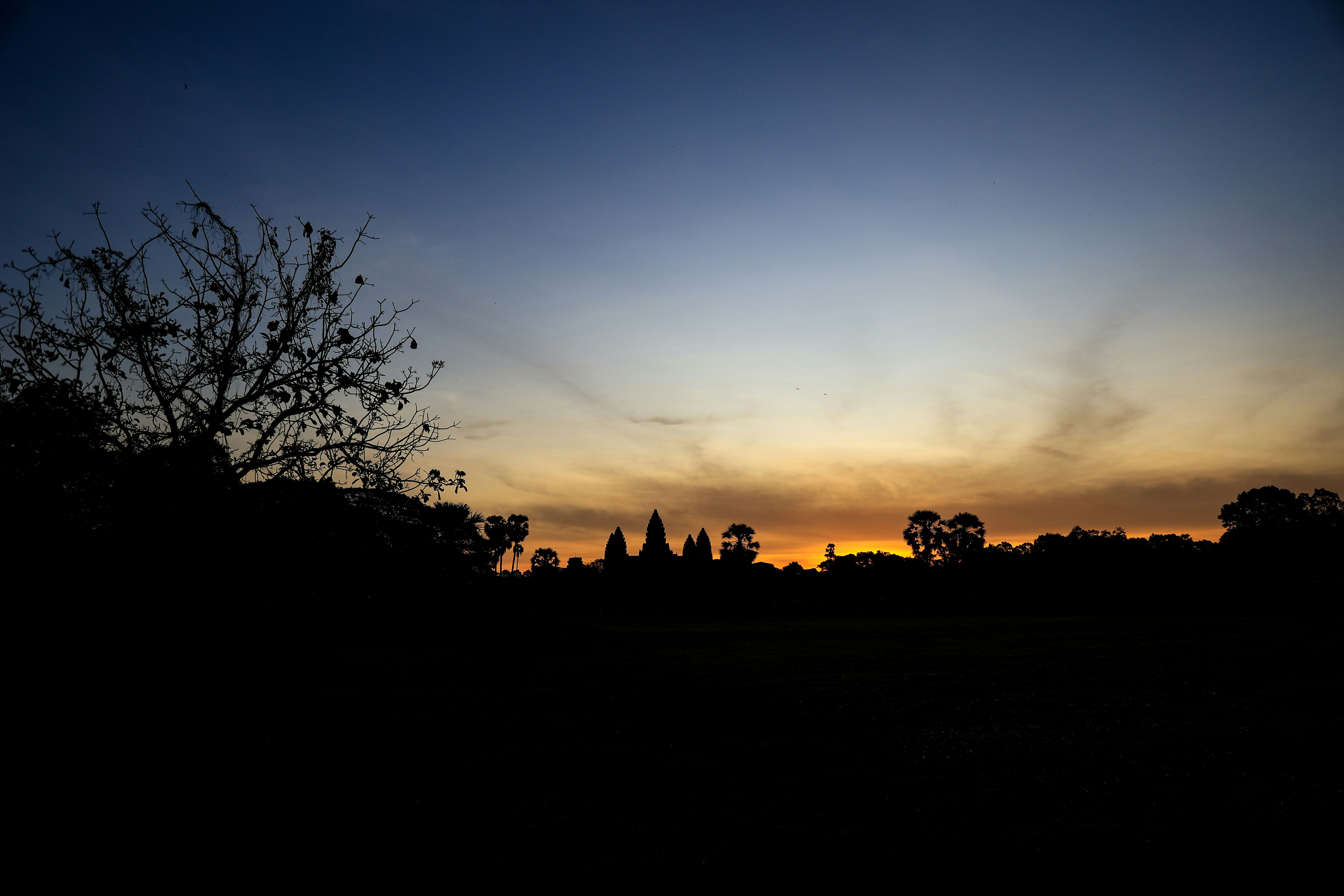 Silhouette of Angkor Wat against a vibrant dawn sky, with trees framing the scene.