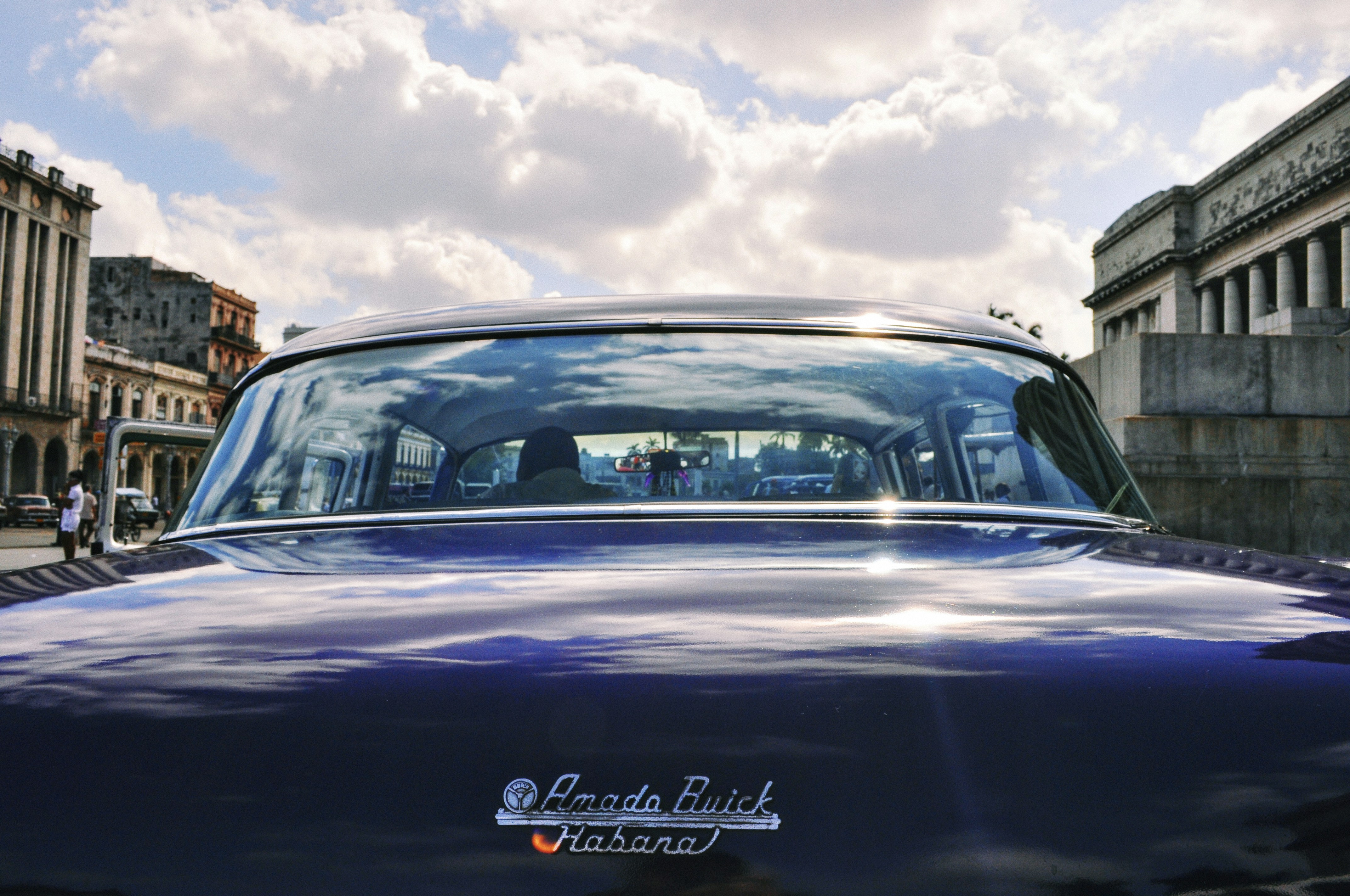 Chrome Badge in Blue: A Vintage Sedan Framed by a Sunlit City Street