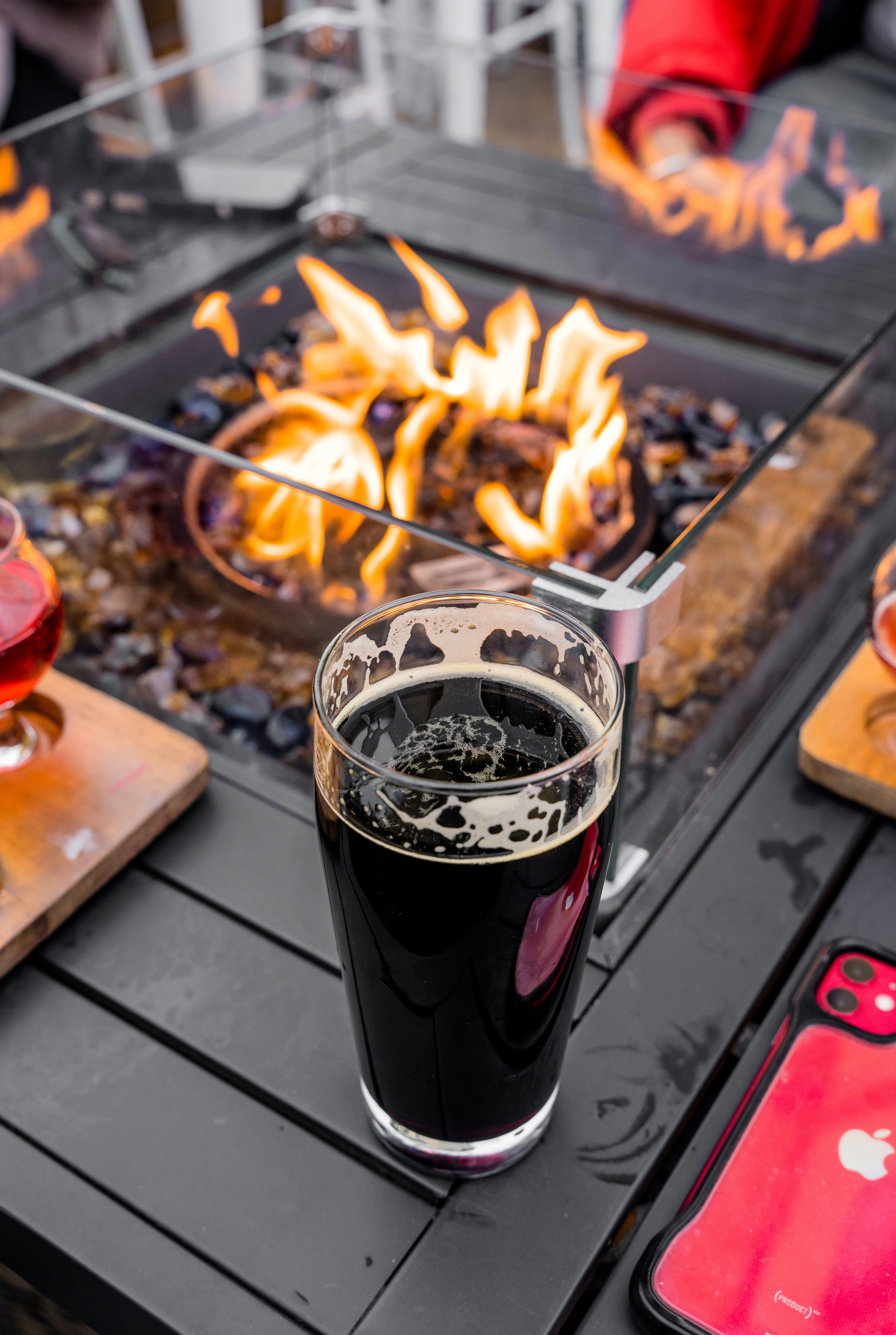Flame-Soft Focus: A Dark Stout Graced by Firelight on a Slatted Terrace Table