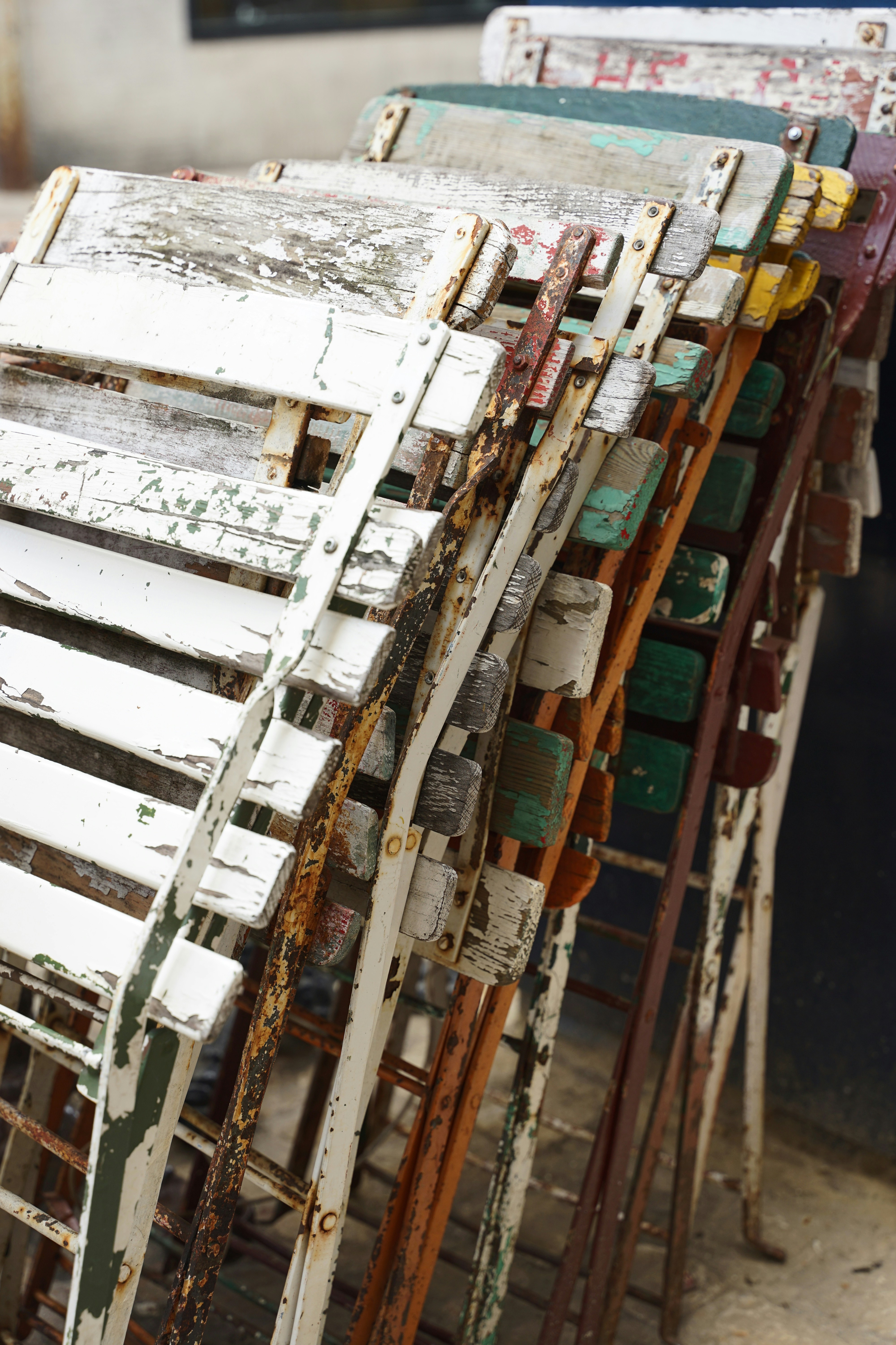 A collection of weathered wooden chairs, stacked and showcasing their rustic charm with peeling paint and patina. The scene evokes a sense of nostalgia.