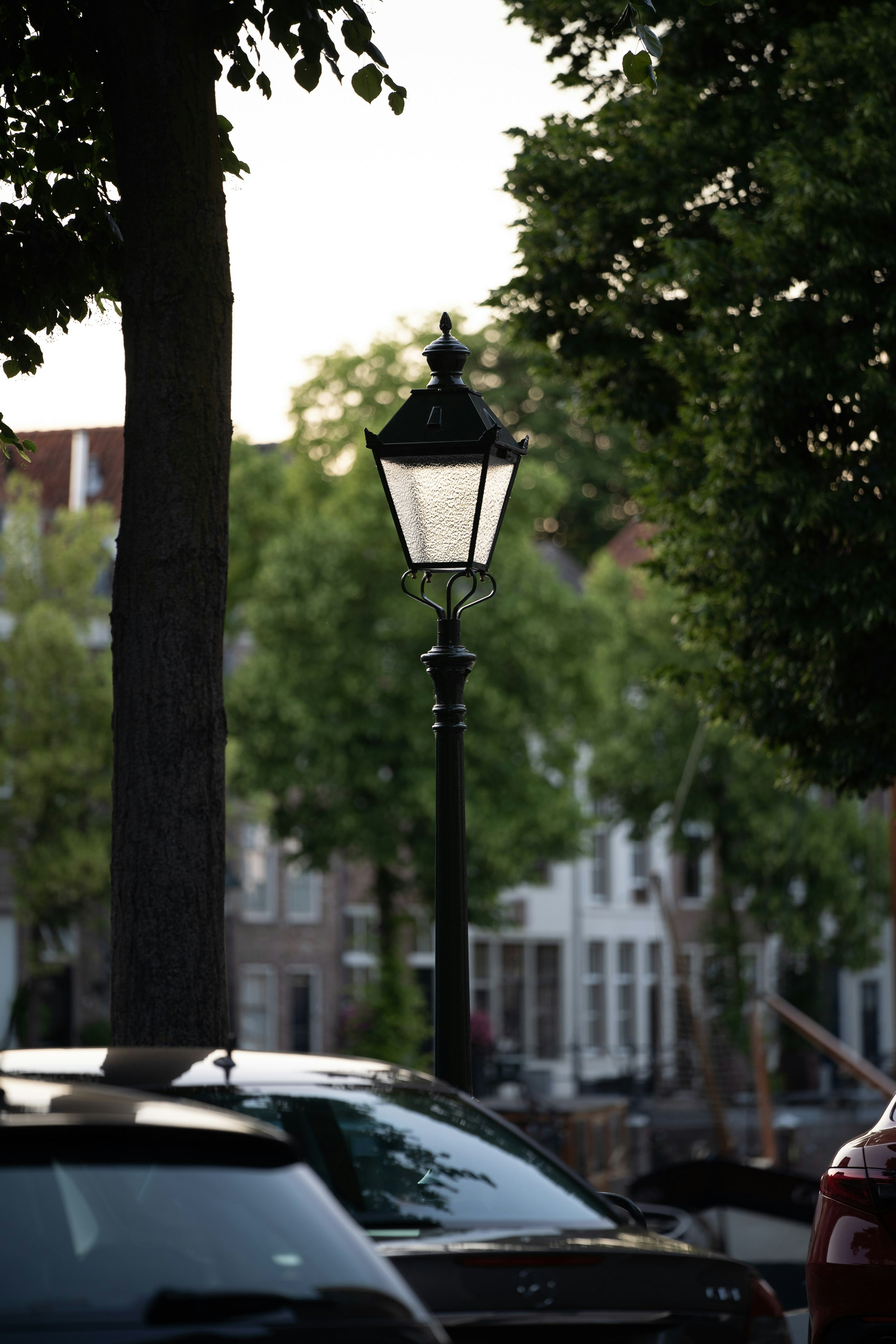 A lamp post on a city street next to parked cars photo – Free ...