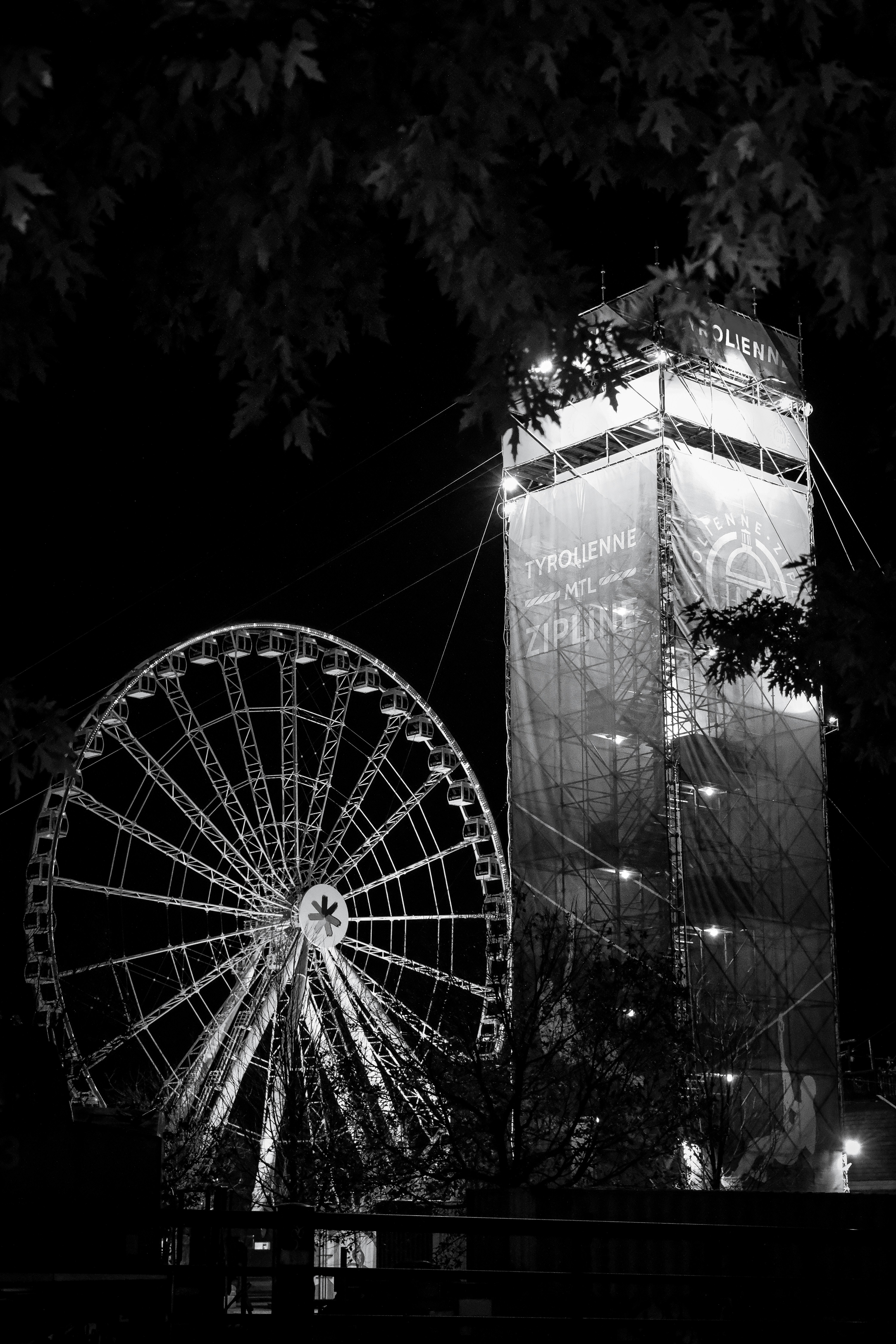 Nocturnal Ferris Wheel beside a towering scaffold under dim city lights