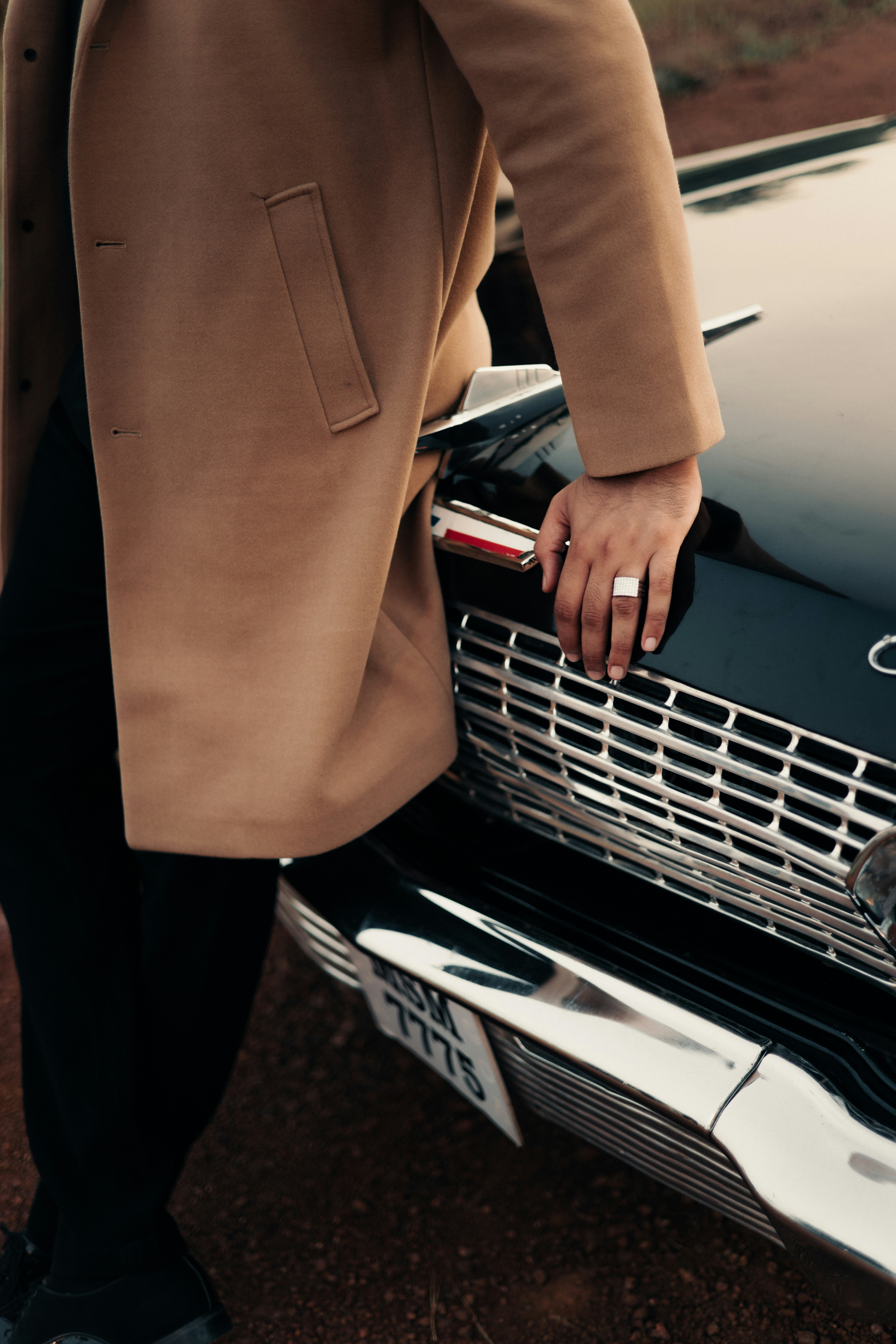 Chrome Quiet: A Tan-Coated Figure at the Grill of a Vintage Car