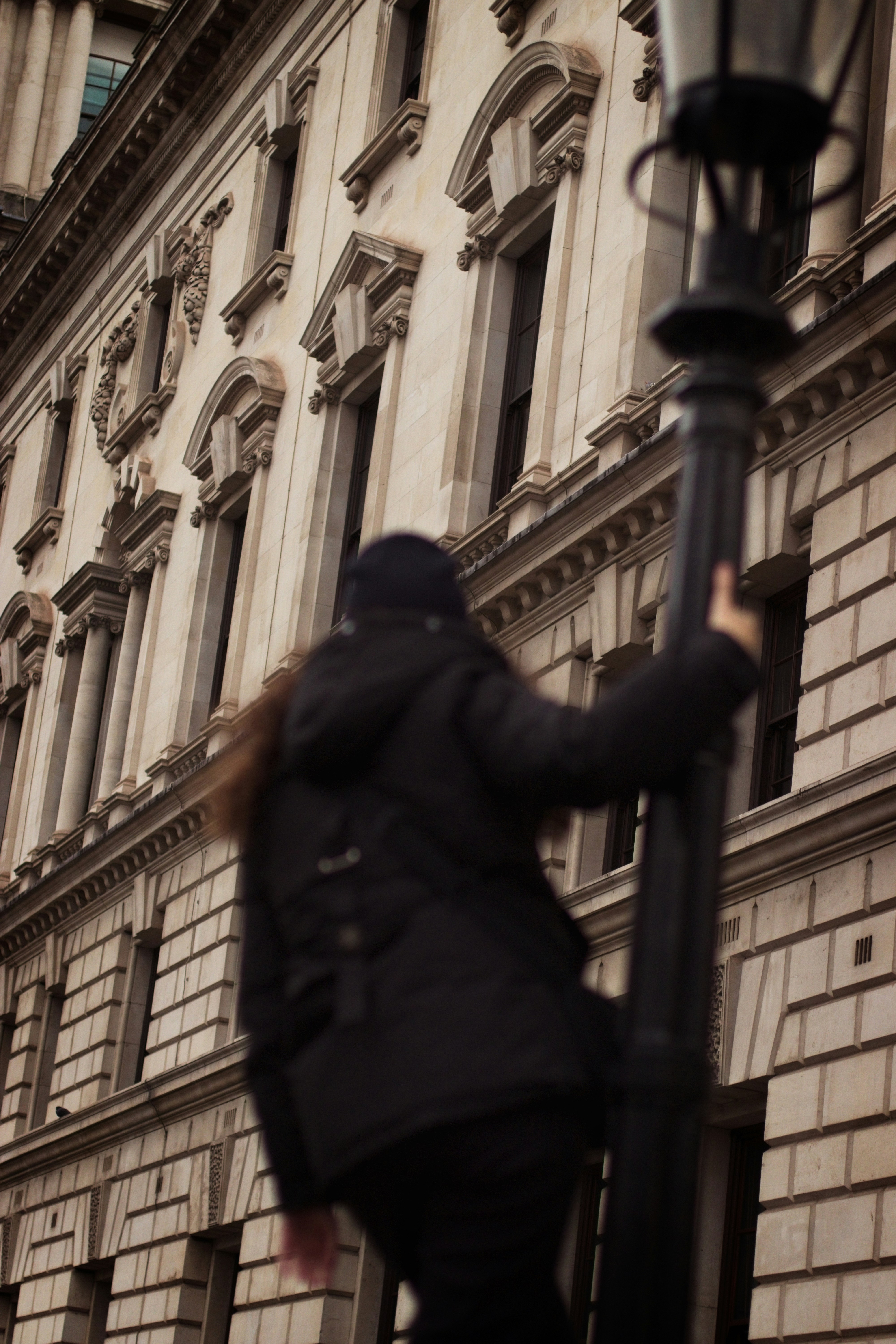Beaux-Arts Ascent: Climber Grips a Streetlamp Beside a Historic Façade