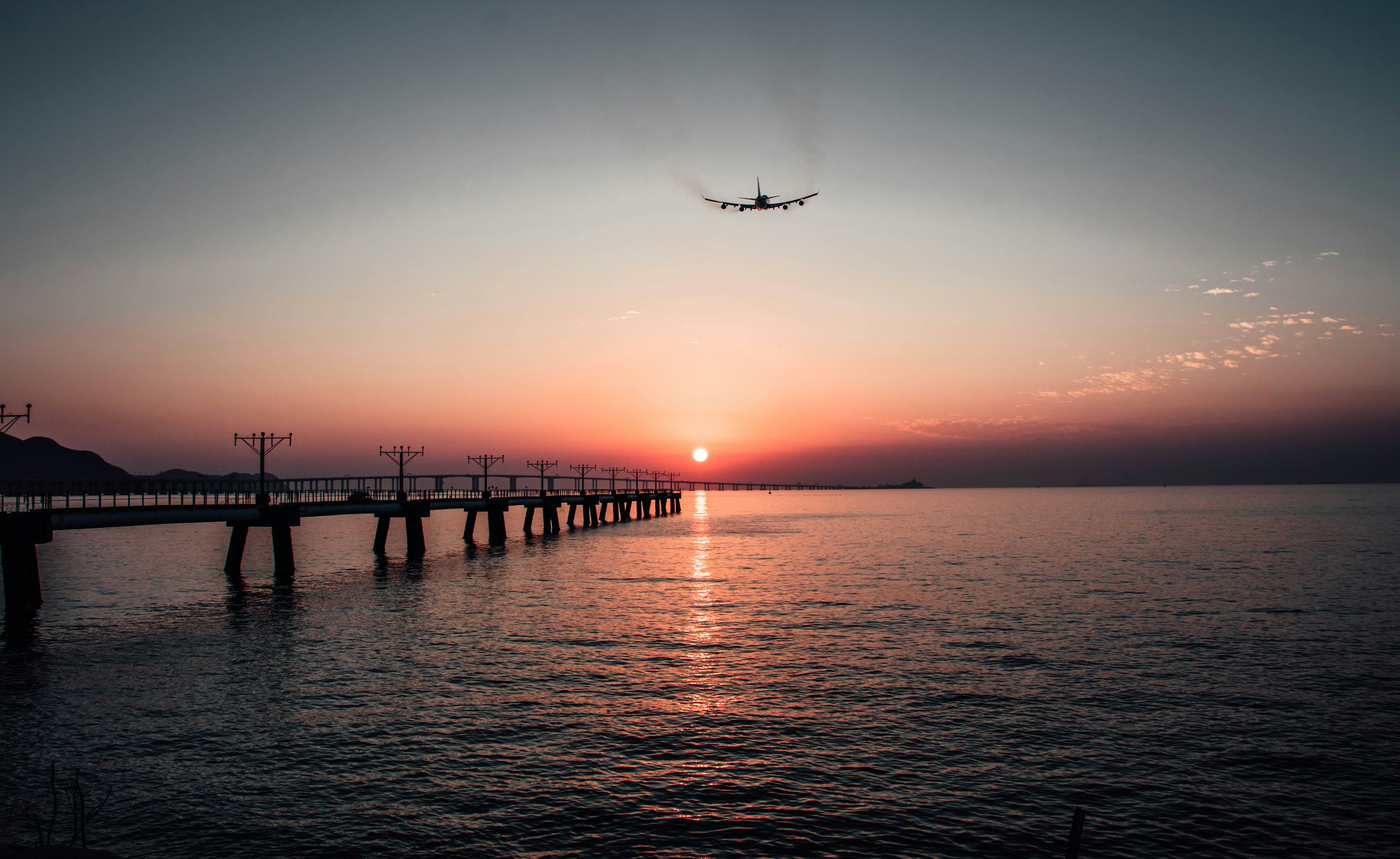 Sunset Flight Over a Quiet Pier as a Jet Arrives at the Horizon