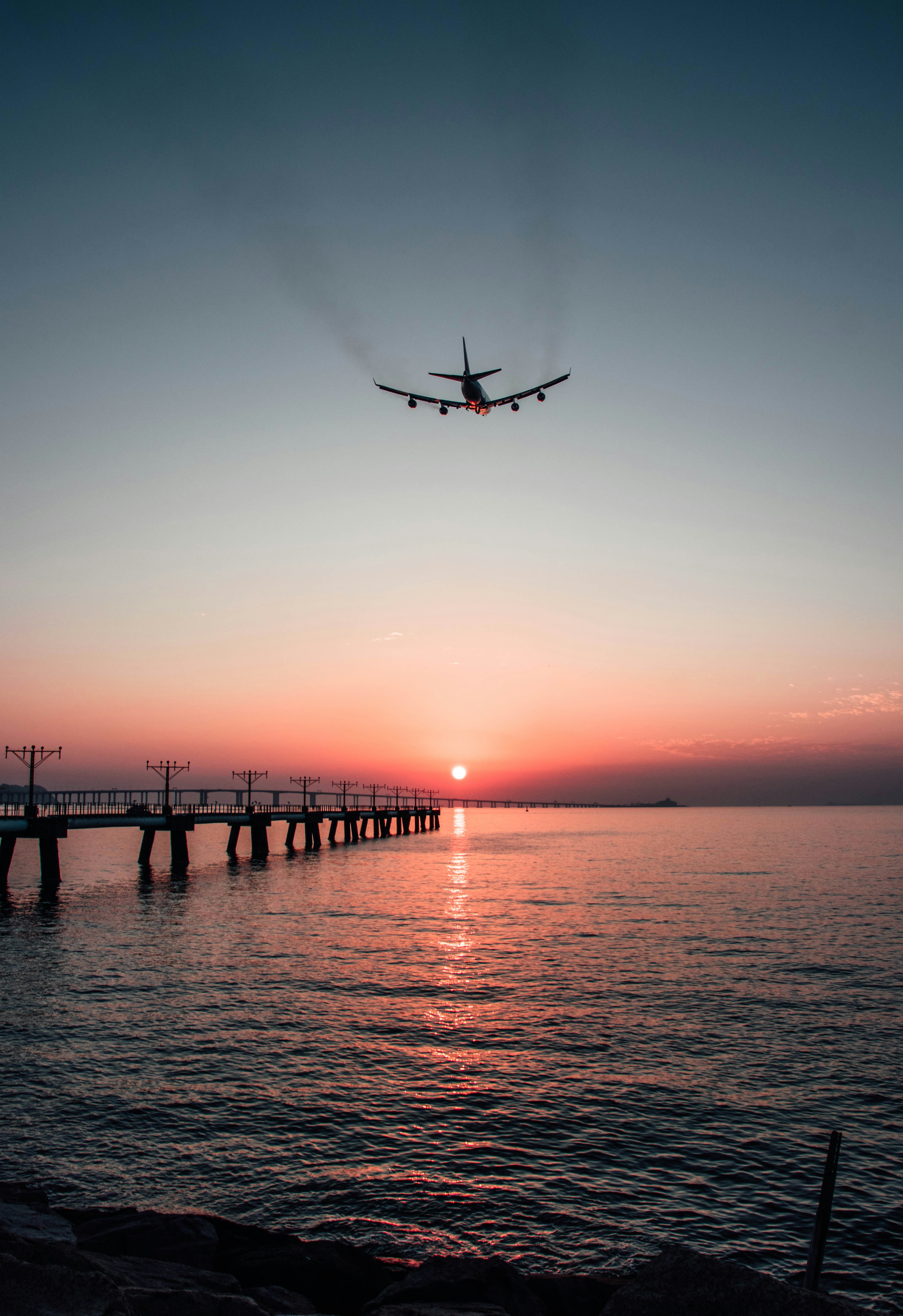 Sunset Approach Above the Pier: A Jet's Silhouette Against Calm Seas