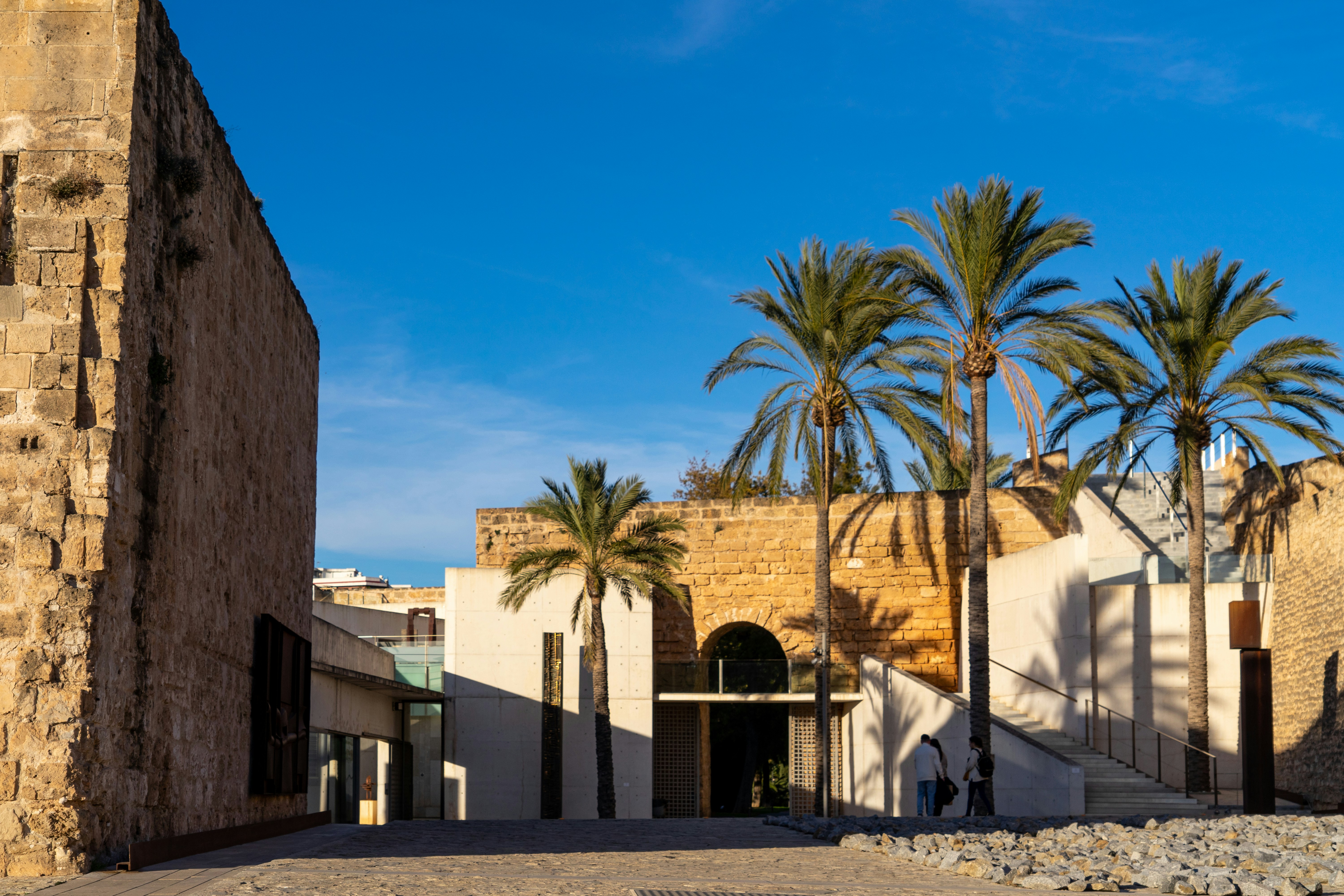 Rustic stone architecture and palm trees under a vivid blue sky.