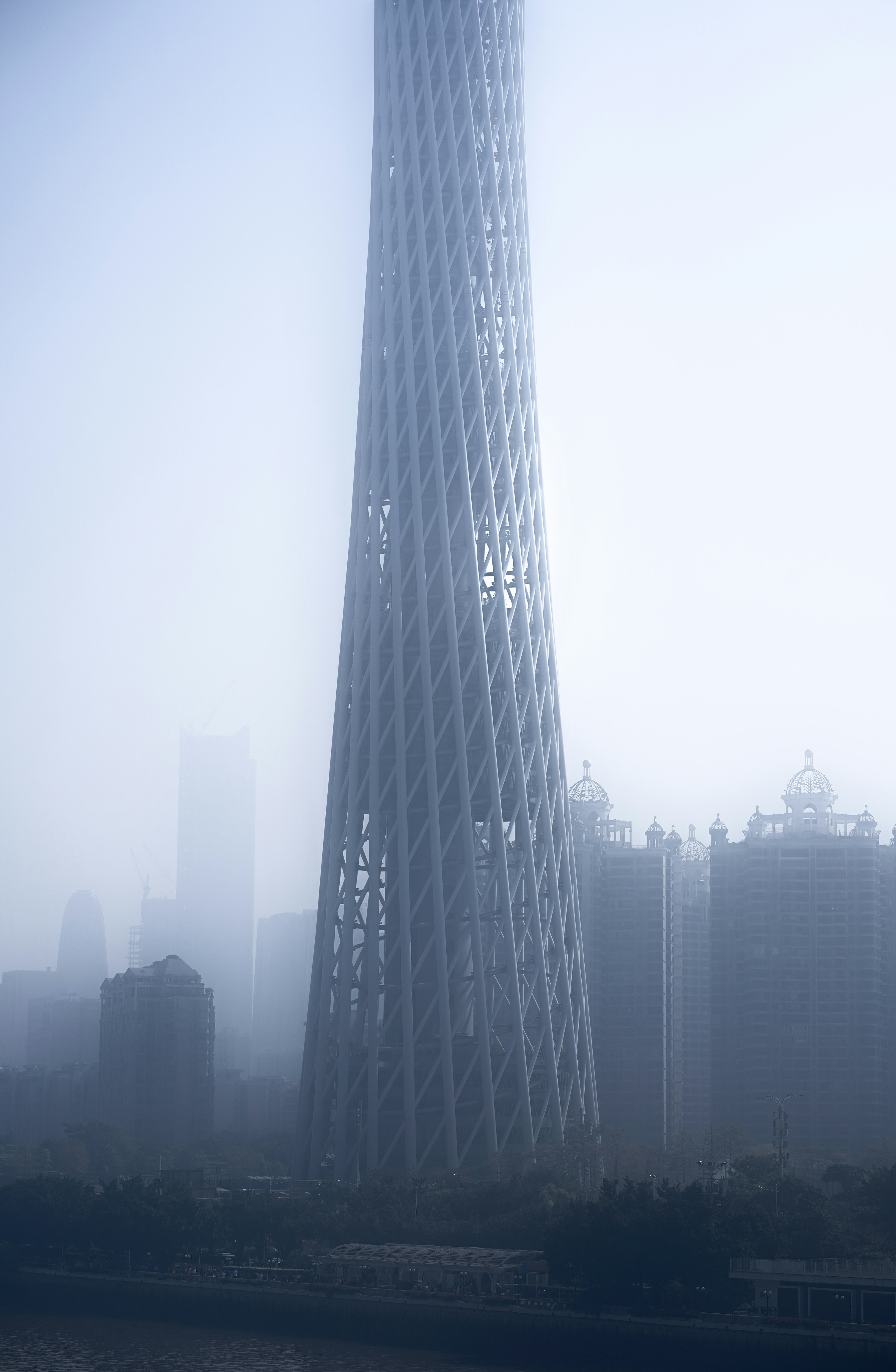 Photograph of a slender lattice tower rising above a foggy city by the river, bathed in cool blue tones.