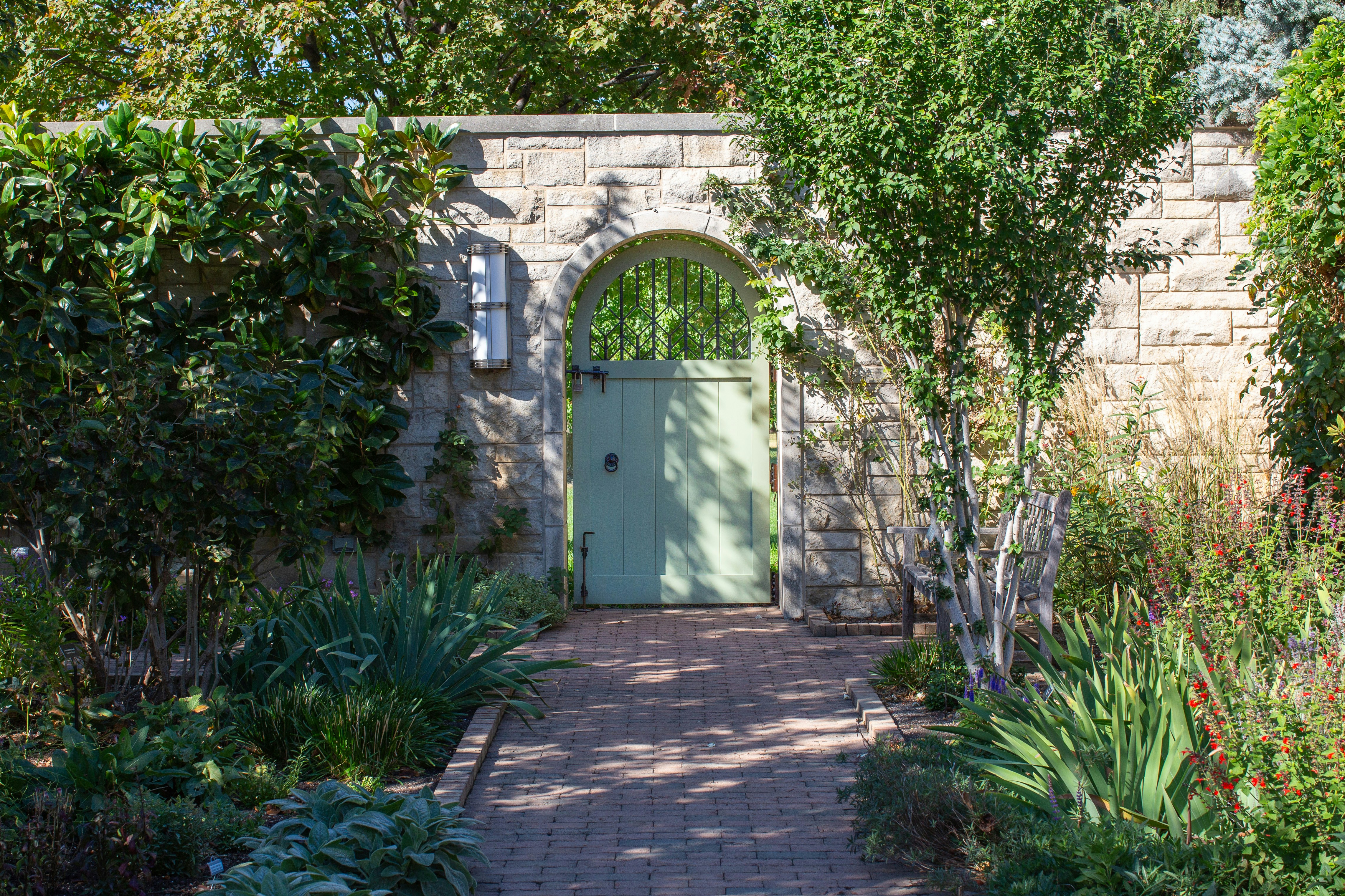 Charming garden entrance featuring a light green door framed by lush greenery and vibrant flowers. A serene pathway invites visitors into the peaceful retreat.