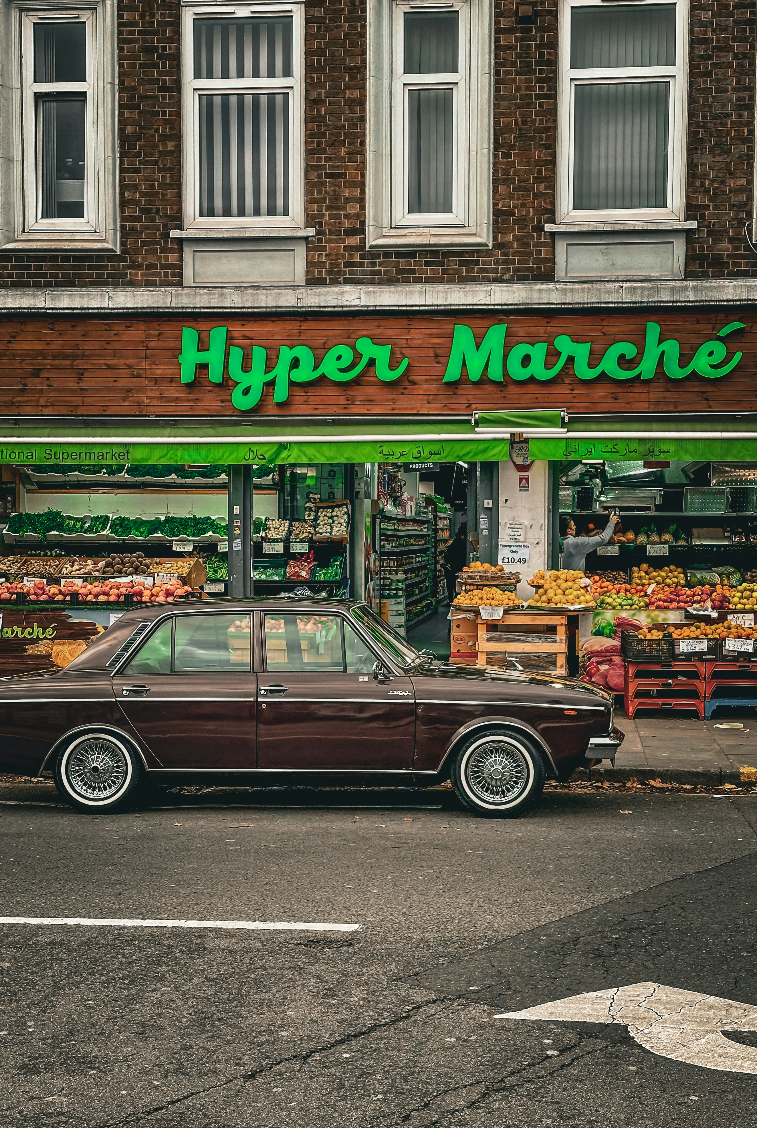 Classic car parked in front of a vibrant grocery store, showcasing an array of fresh produce and colorful signage.