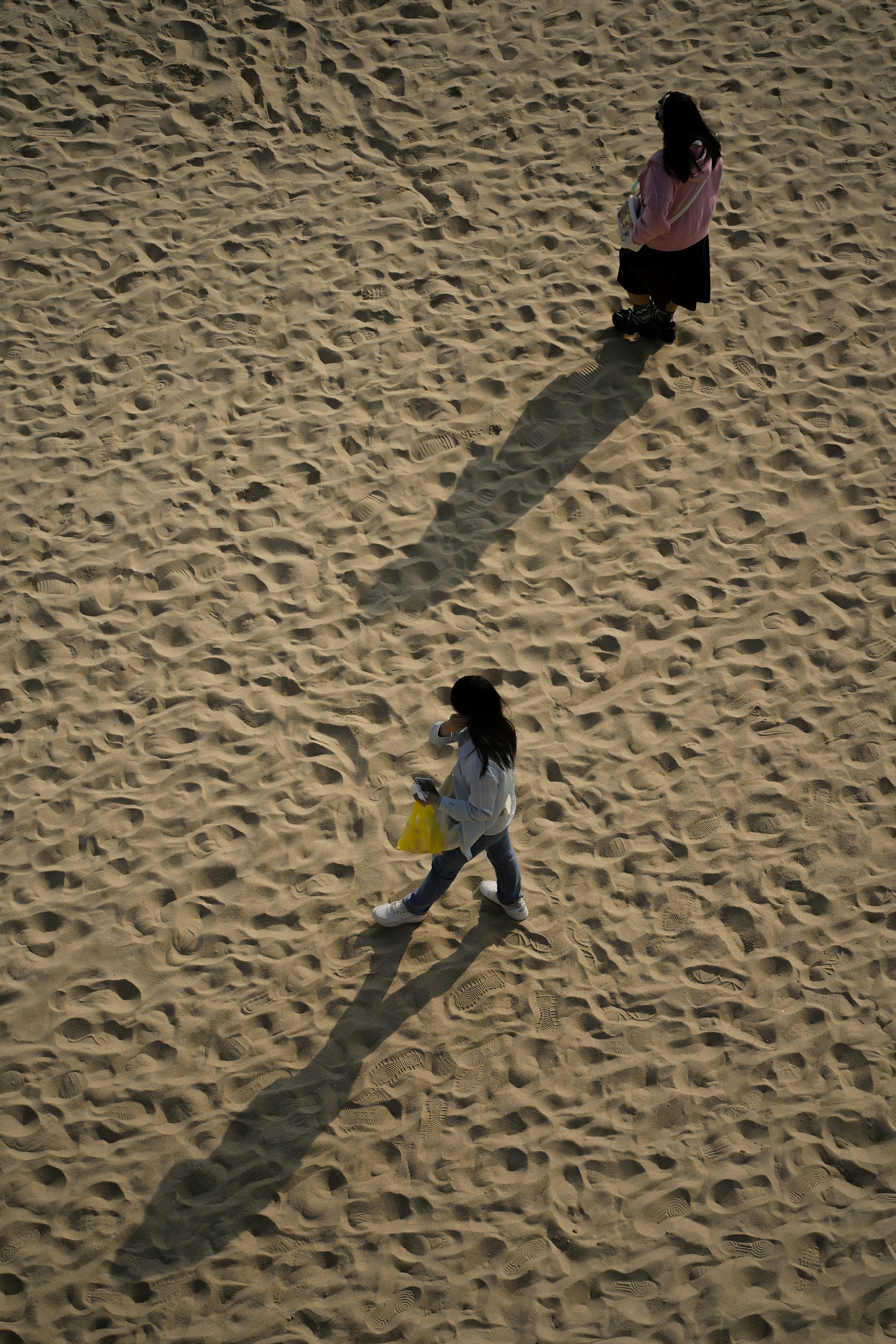 Shadow Diagonal: Two Beach Walkers Cast Long Lines Across Textured Sand