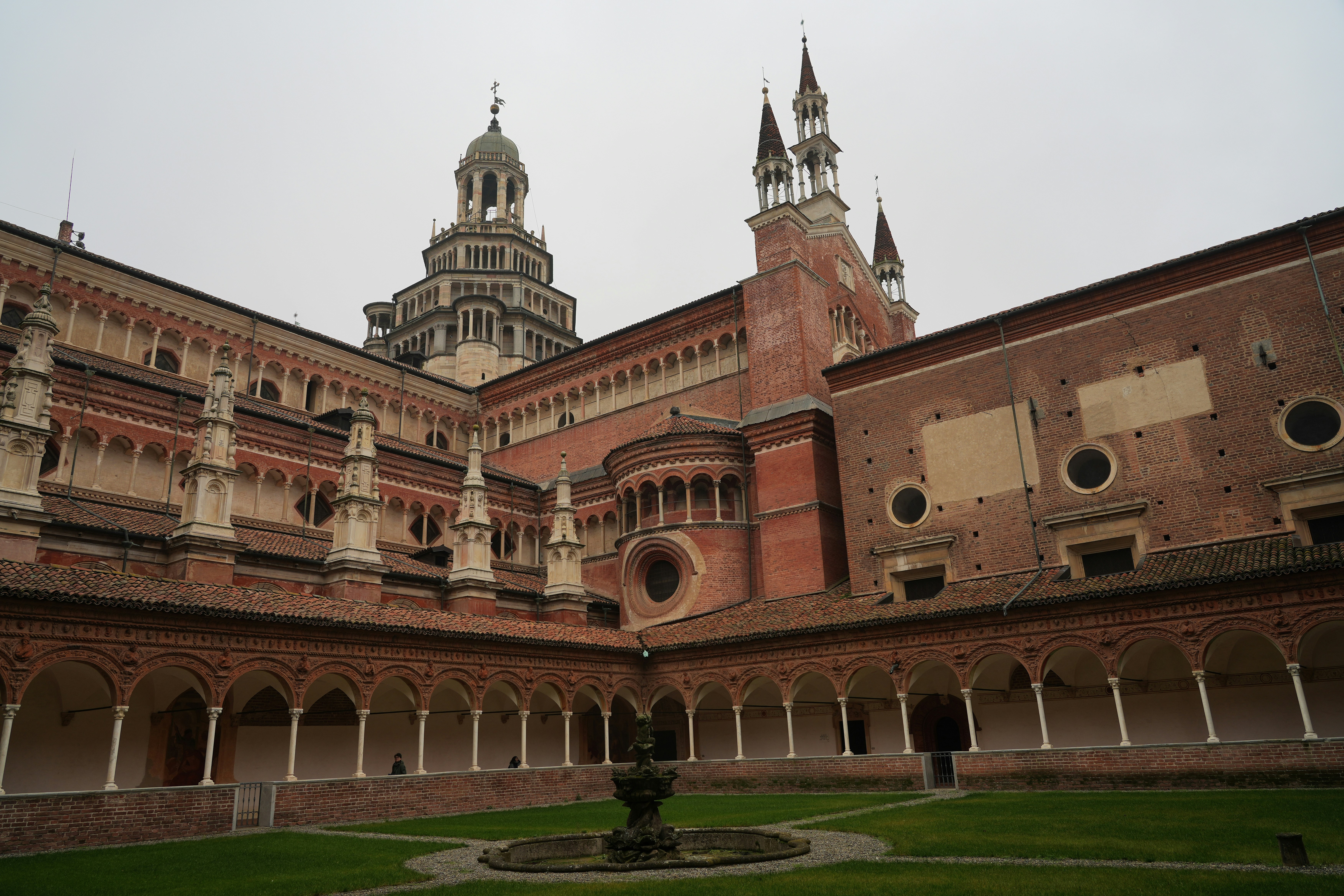 Historic cloister courtyard of Certosa di Pavia with intricate stonework and towering spires.