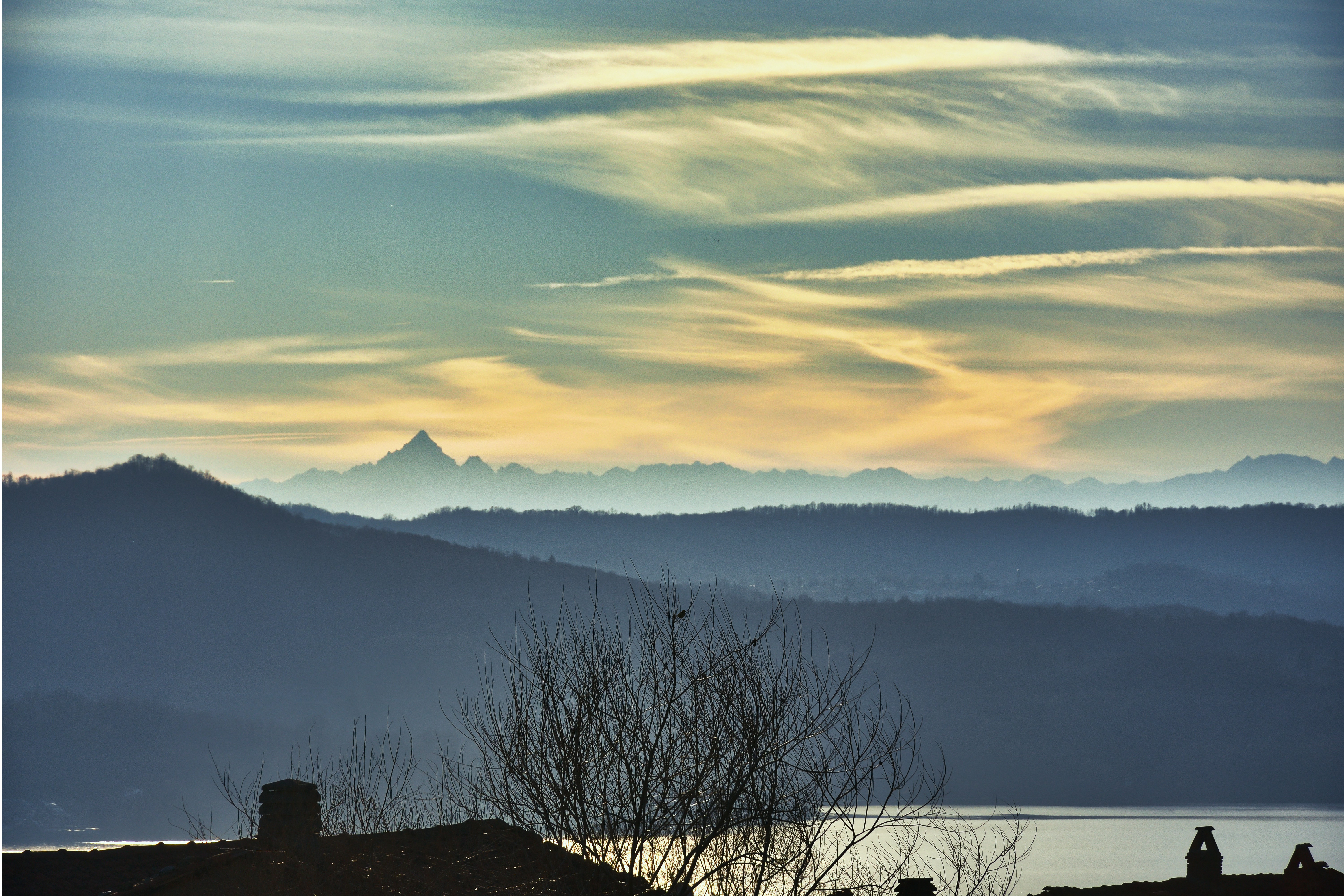 Silhouetted mountains and delicate clouds over Viverone Lake at sunset.