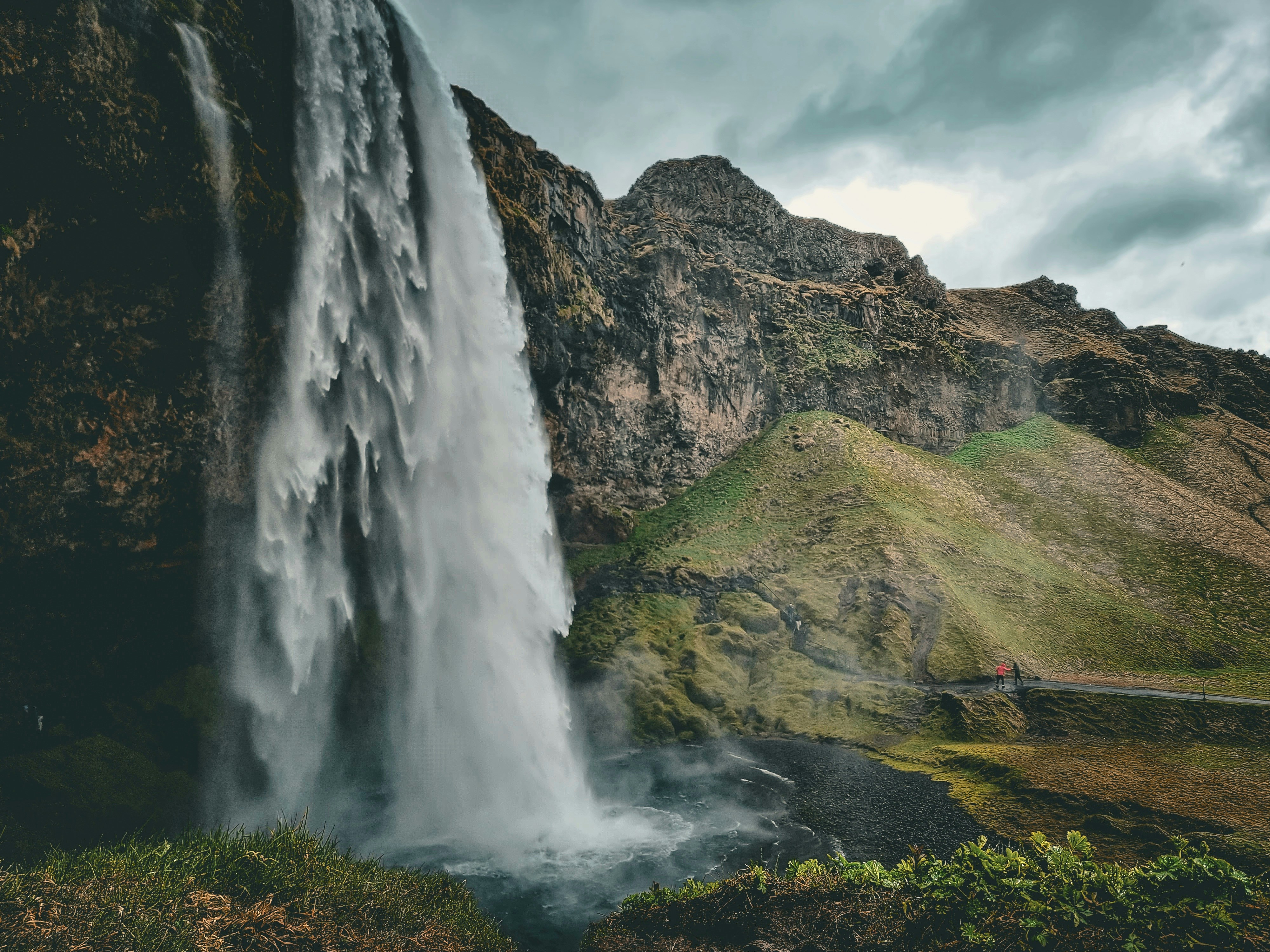 A very tall waterfall with a man standing next to it photo – Free ...