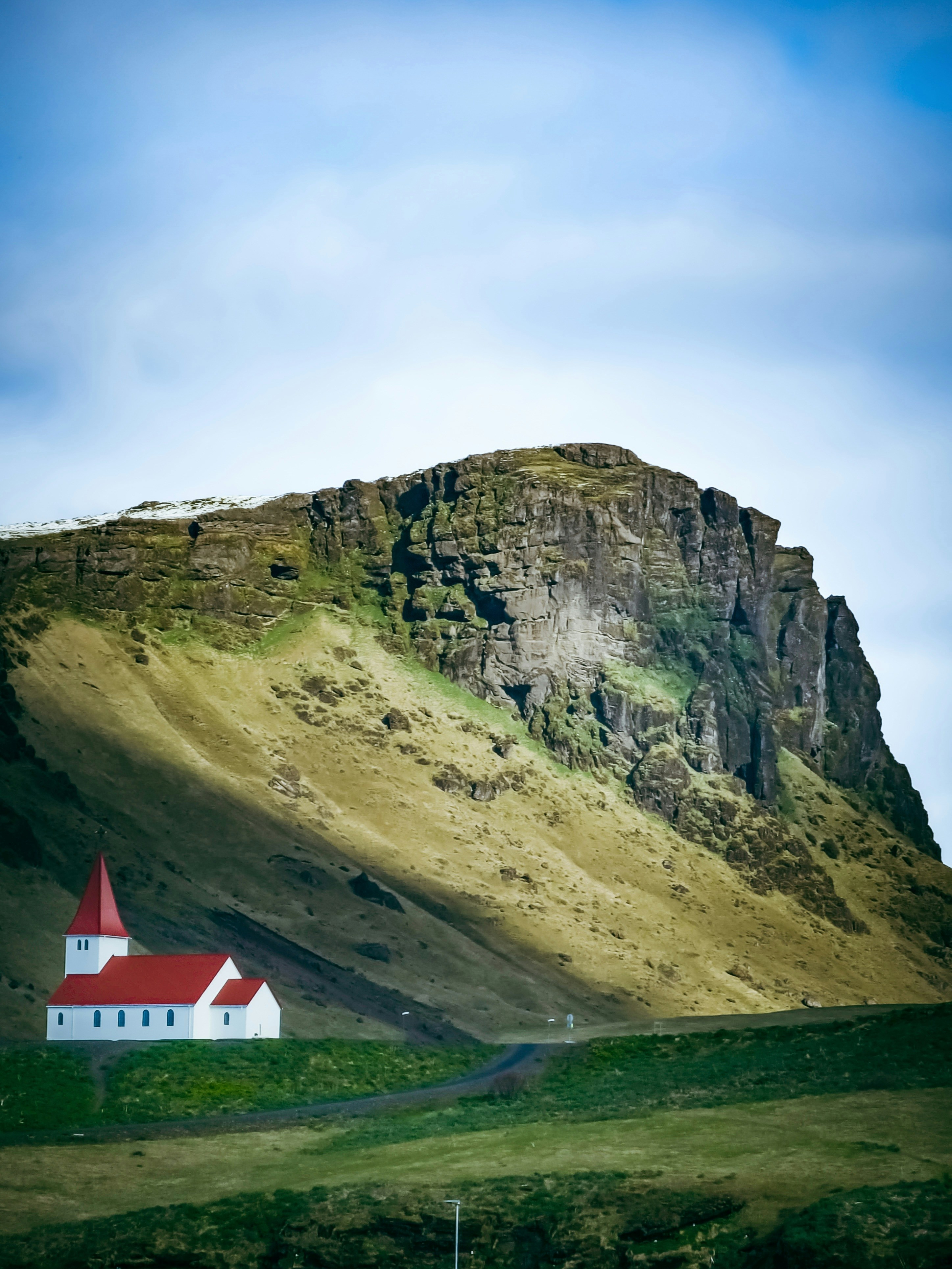 Crimson-roofed Chapel at the Foot of a Rugged Cliff Under a Clear Blue Sky