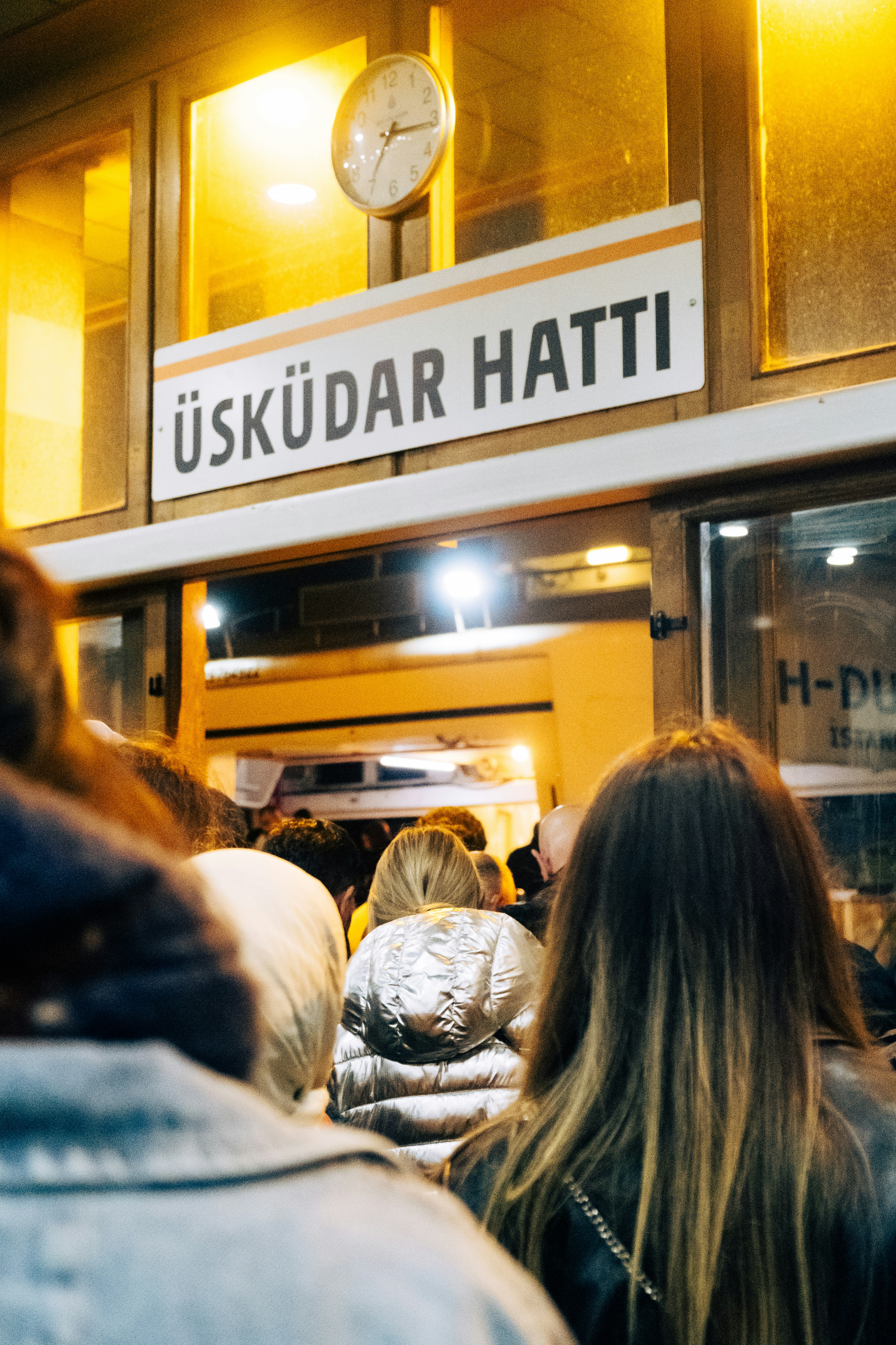 Crowd gathered at the Üsküdar Hatti entrance, showcasing the hustle of urban life. A clock on the wall indicates the passage of time amidst the waiting crowd.
