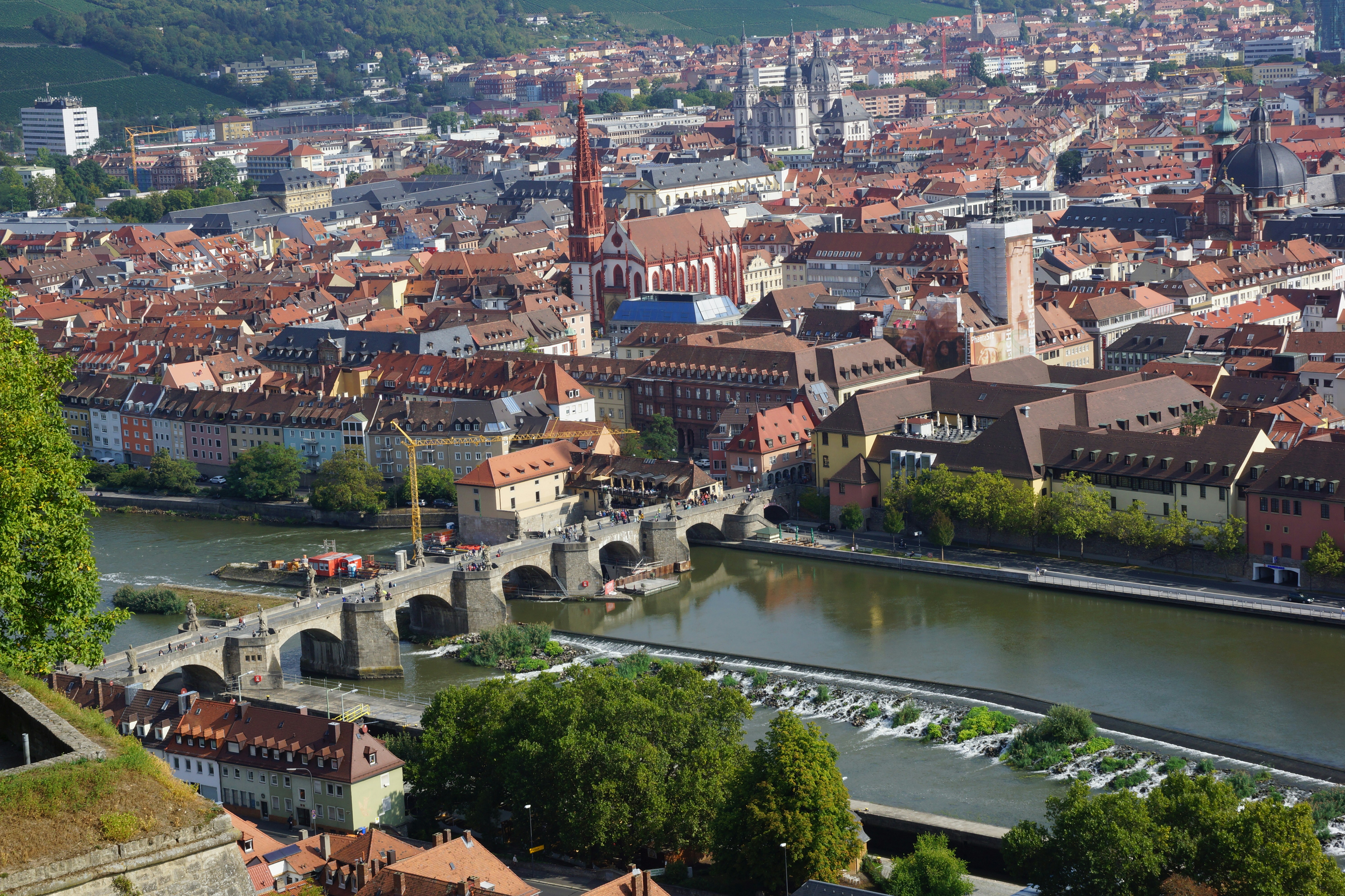 Riverside cityscape featuring a historic stone bridge crossing a meandering river under a clear sky.