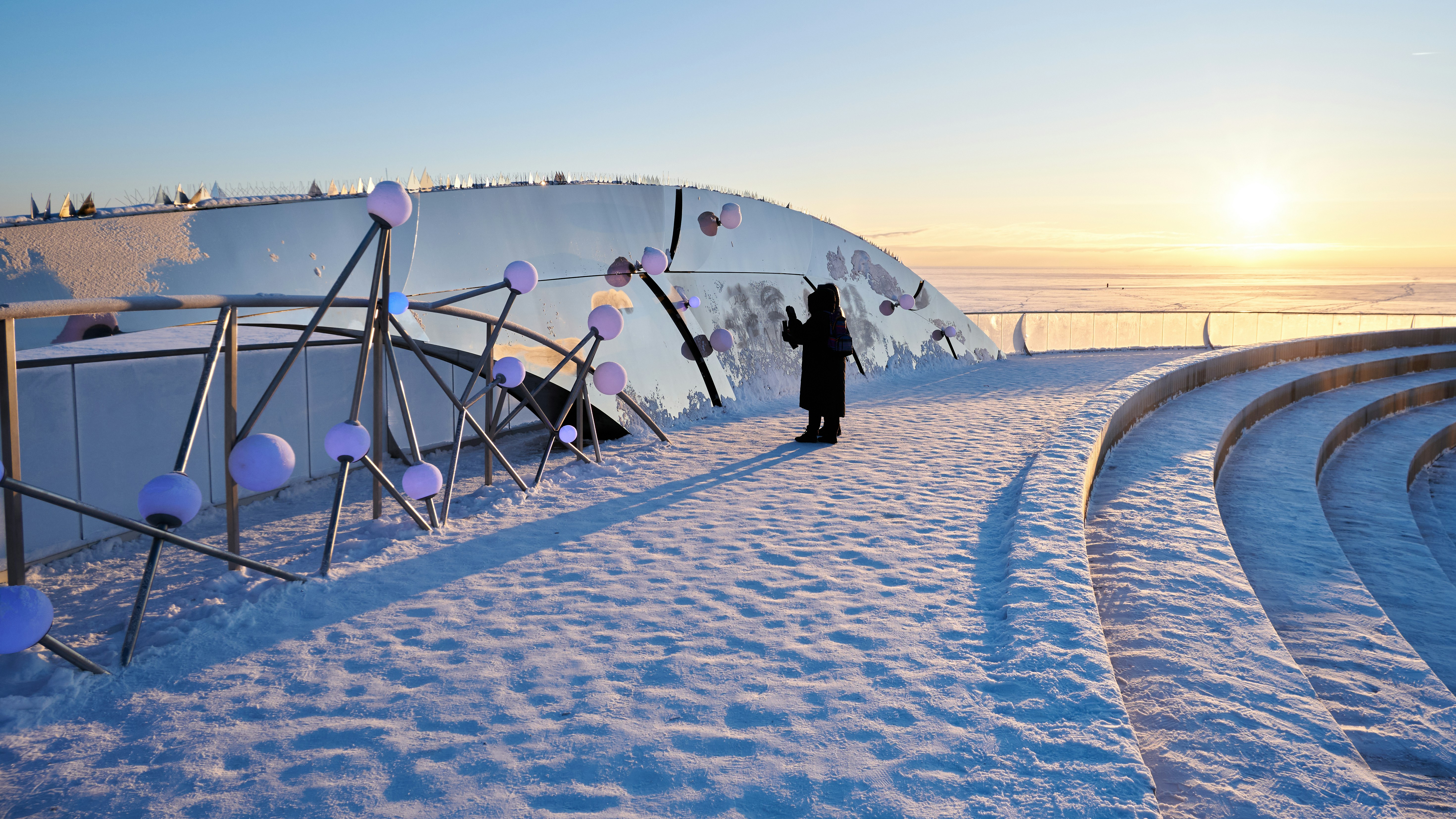 Lone Figure beside a Violet Orb Sculpture on a Snow-Covered Promenade at Sunset
