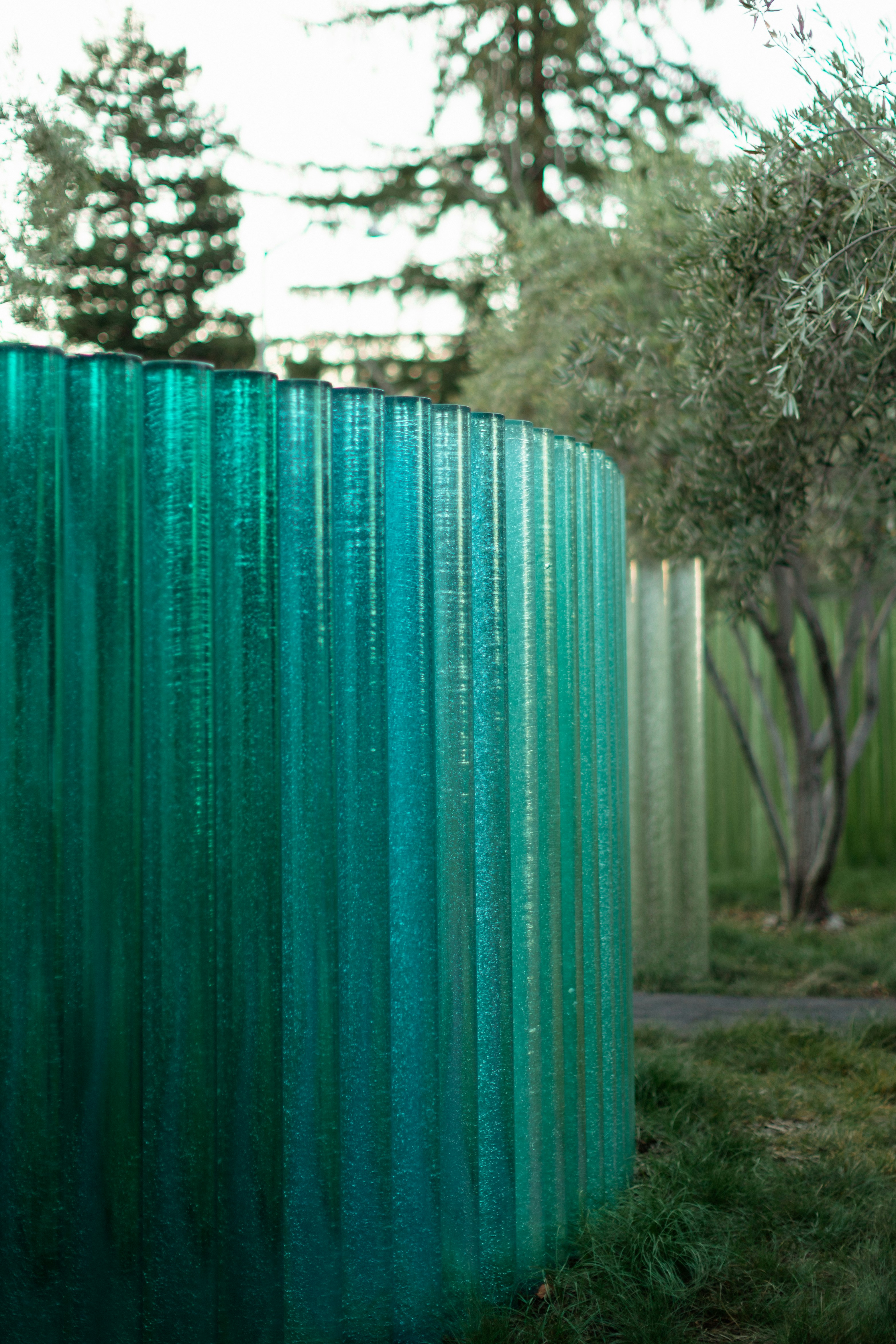 Teal Glass Fence: Vertical Light Stripes in a Quiet Park