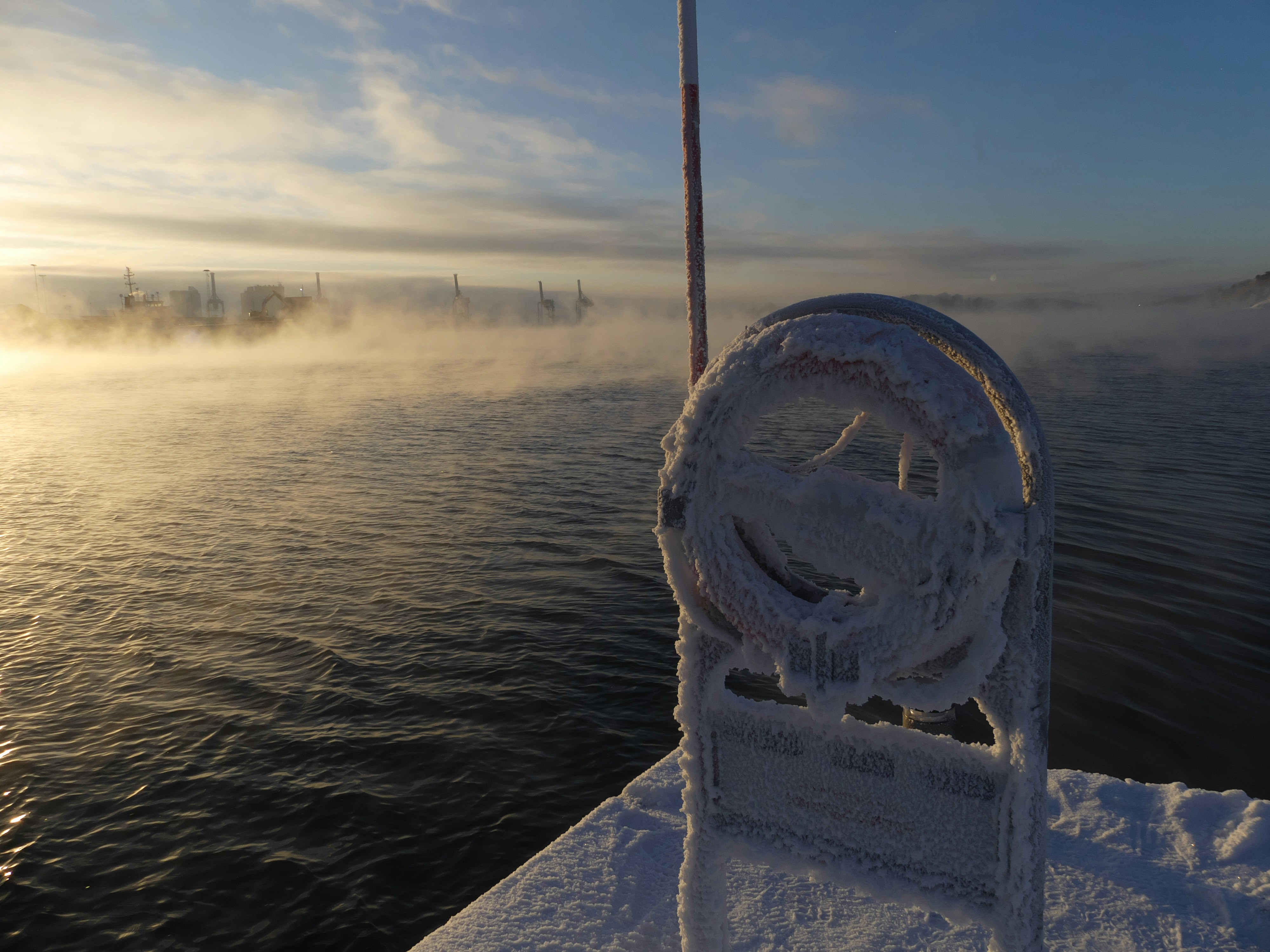 Dawn Frost on the Dock: An Ice-Covered Winch Reaching Toward Misty Waters