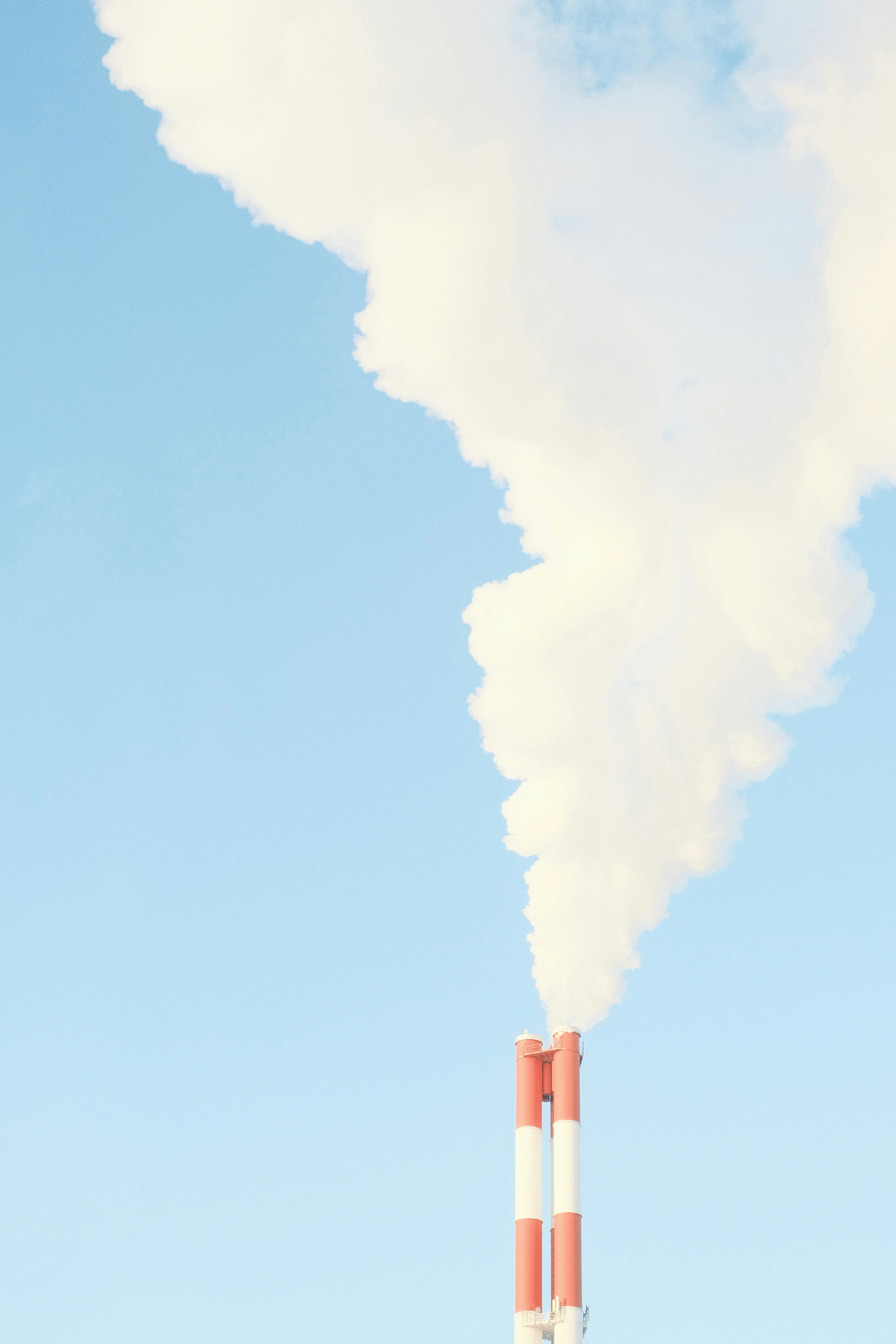 A smokestack emits from a pipe in front of a blue sky photo – Free ...