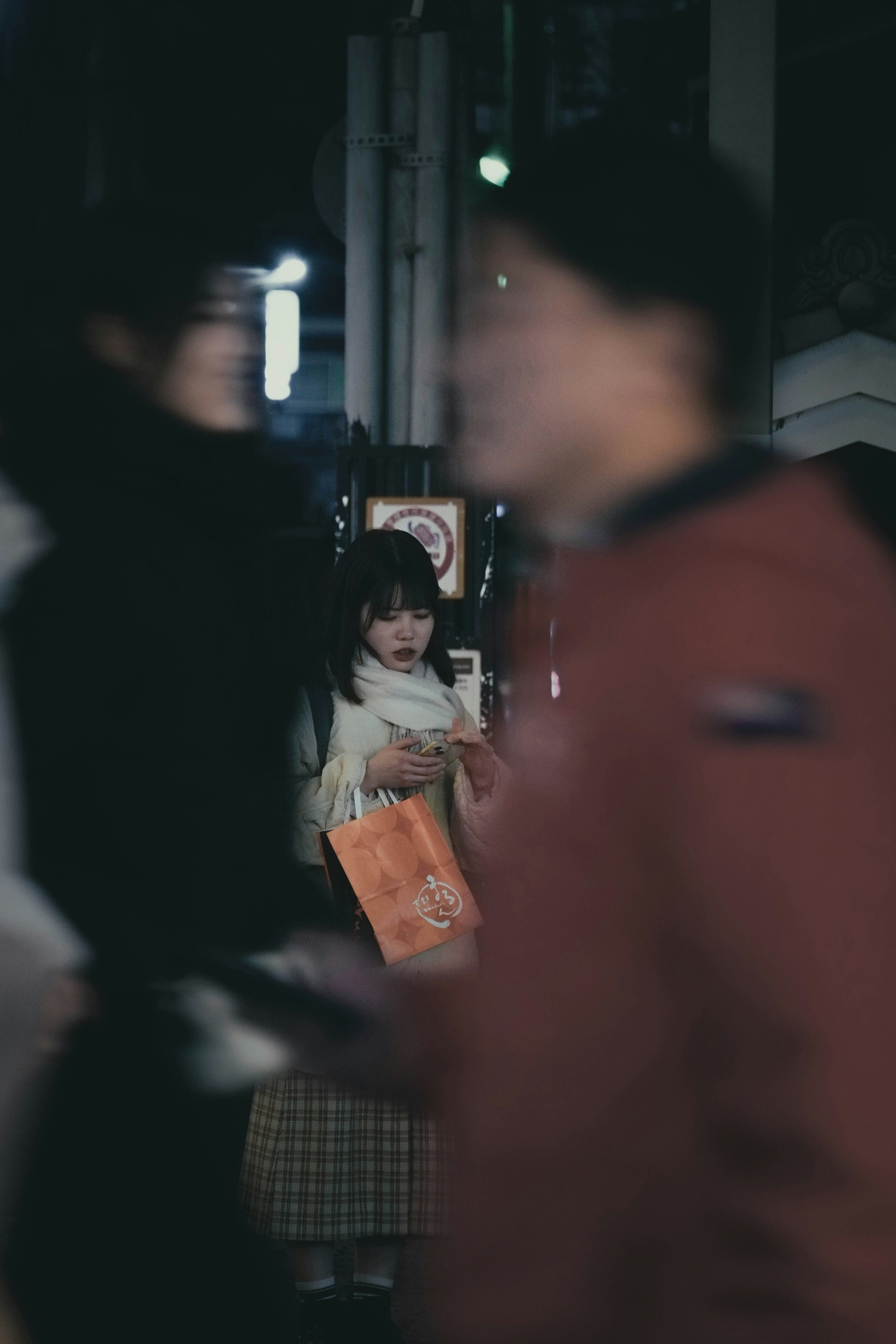 Midnight Pause: The Girl with the Orange Bag Amid Moving Faces