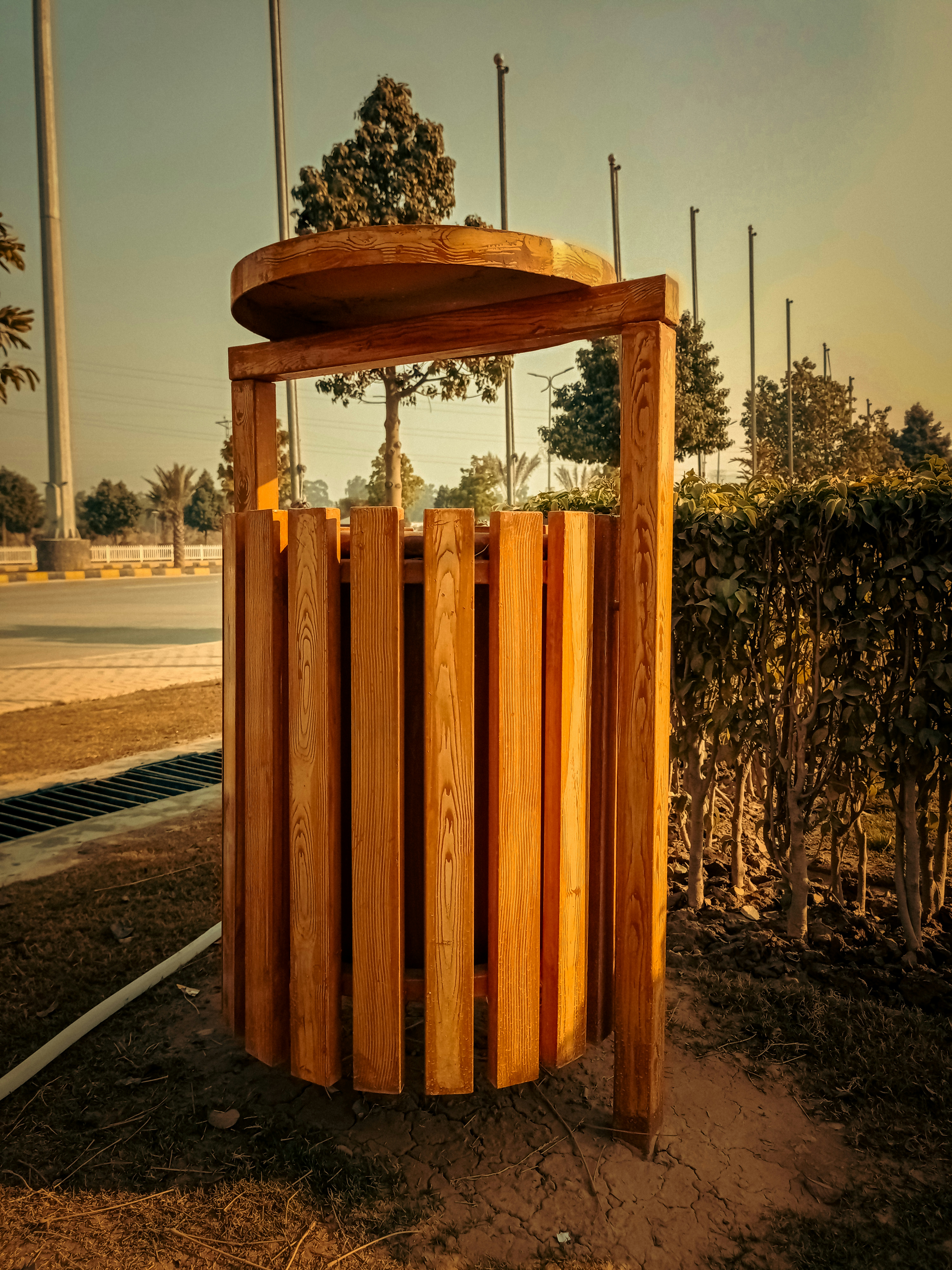 A beautifully crafted wooden trash bin stands amidst greenery, showcasing an eco-friendly design that blends with the natural environment.