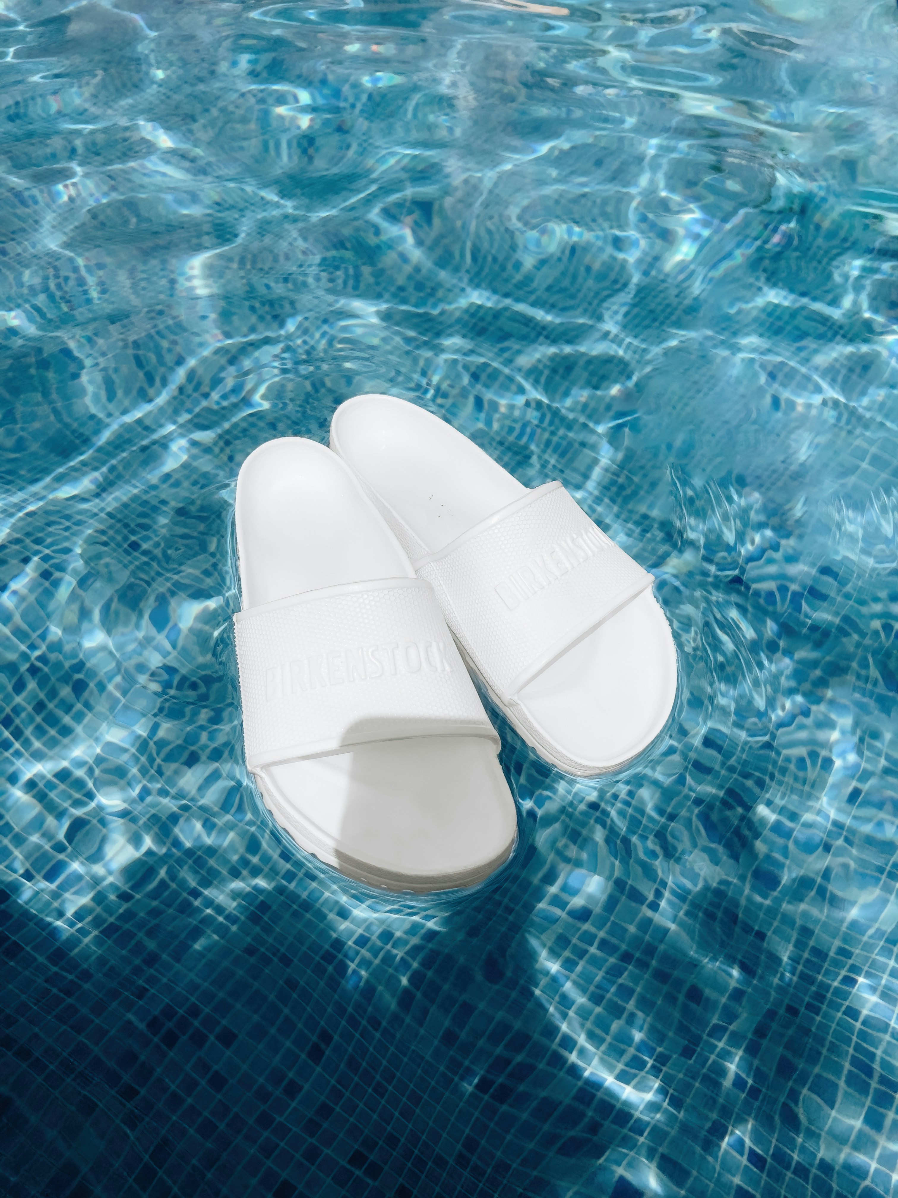 A pair of white slippers floating in a pool of water photo – Free ...