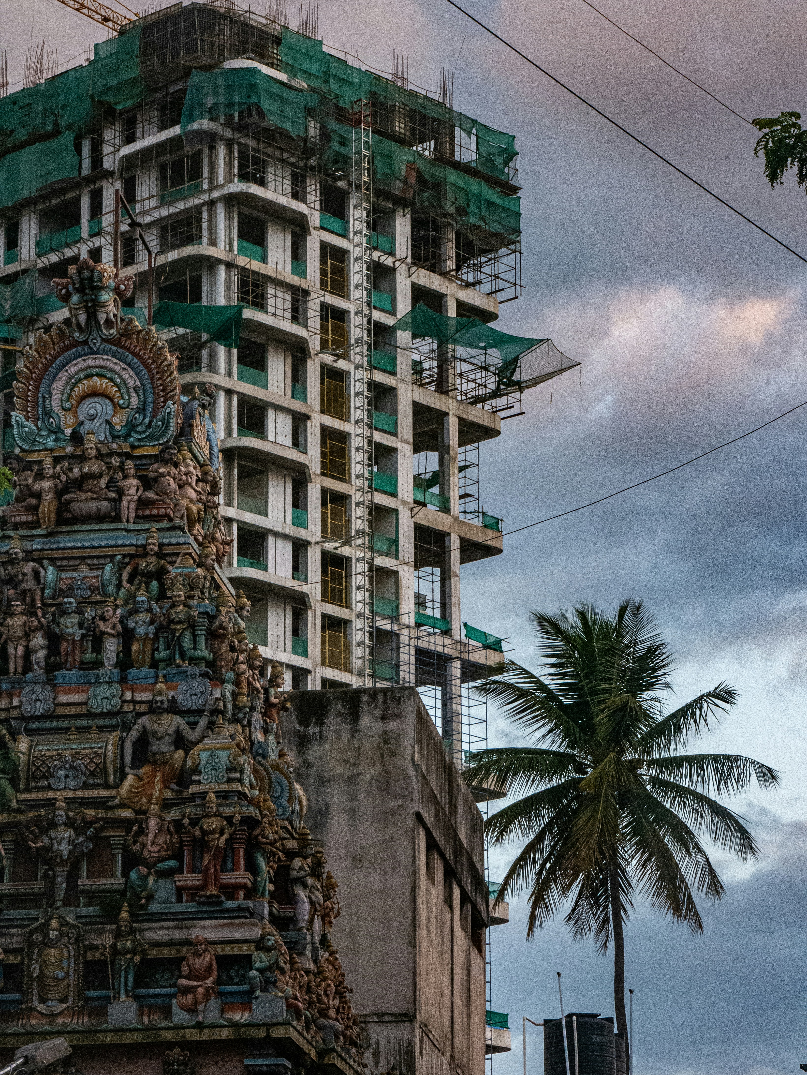 A striking contrast of modern high-rises and traditional Hindu temples in the heart of Bangalore, India, where towering buildings stand beside lush palm trees under a vibrant sky. The city’s dynamic blend of urban development and cultural heritage creates a unique and captivating skyline in Karnataka’s bustling metropolis. | a very tall building with a clock on it's side