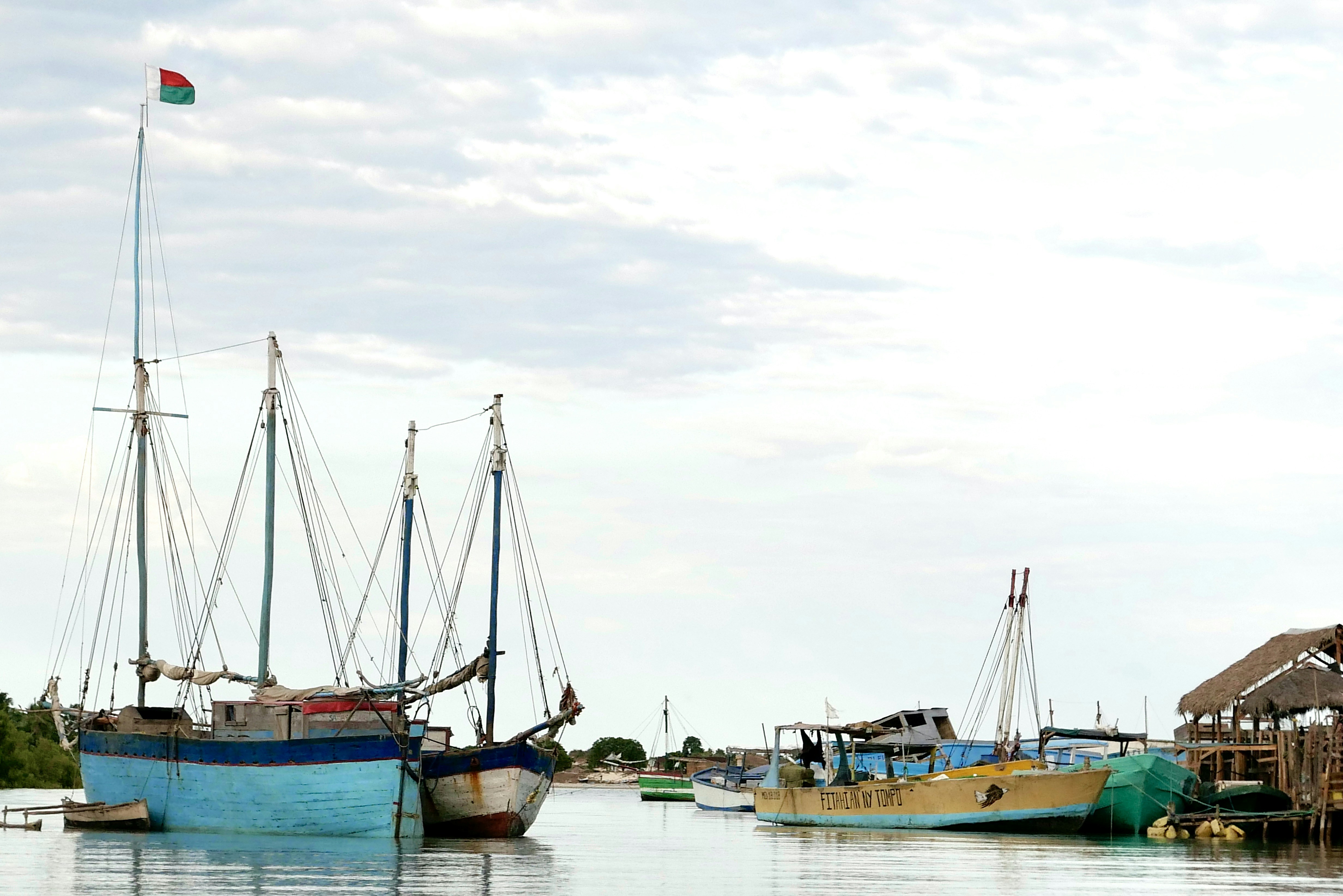 Colorful boats anchored peacefully under a cloudy sky near a coastal village.