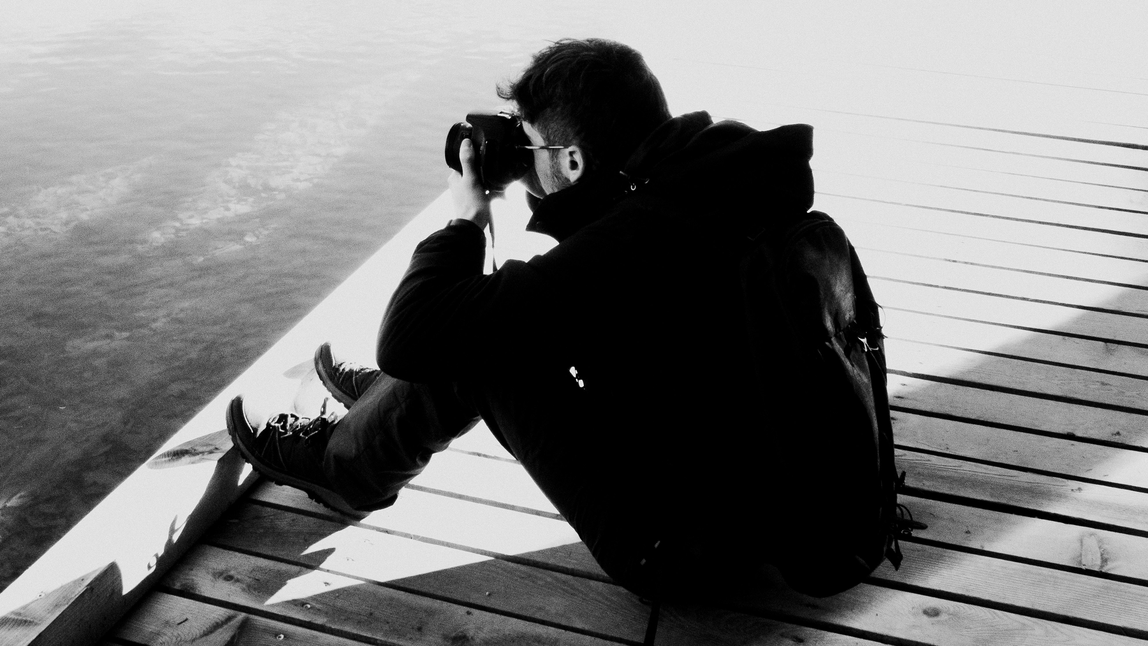 Silhouetted figure of a photographer sitting on a wooden dock by the water.