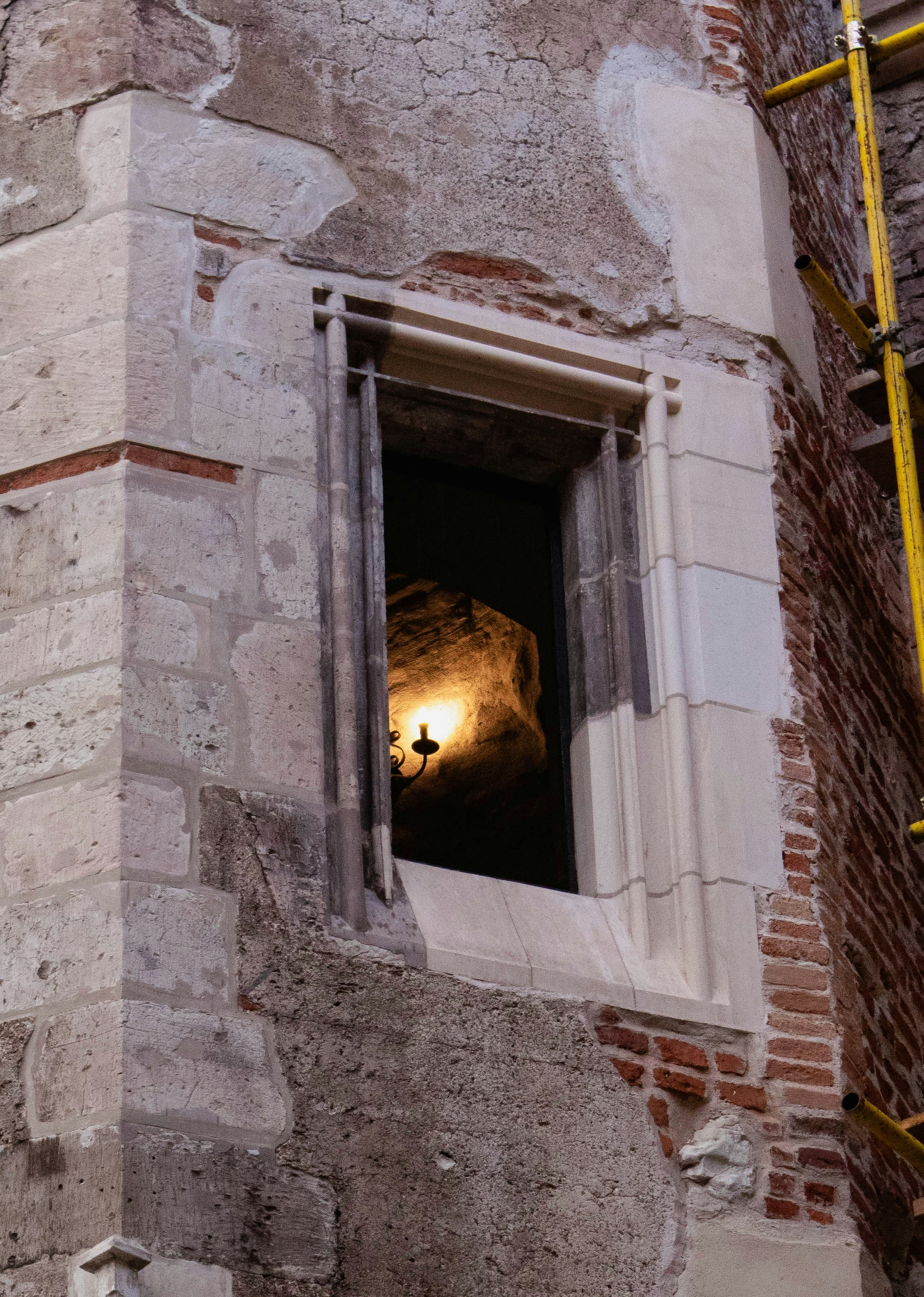 Lantern Glow Through a Narrow Window in Weathered Stone Facade