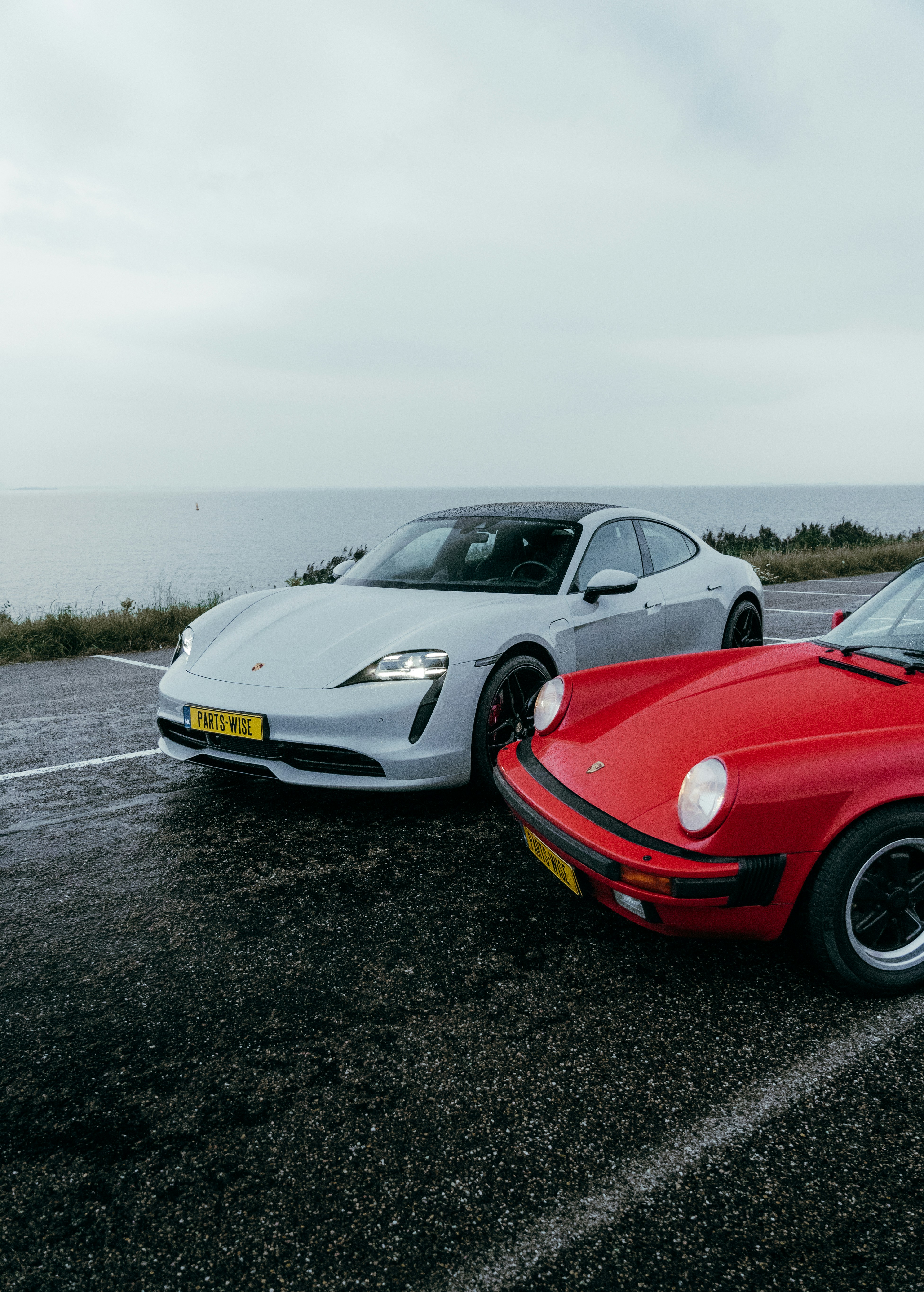 Coastal Convergence: White Porsche 911 beside a Red Classic by the Sea