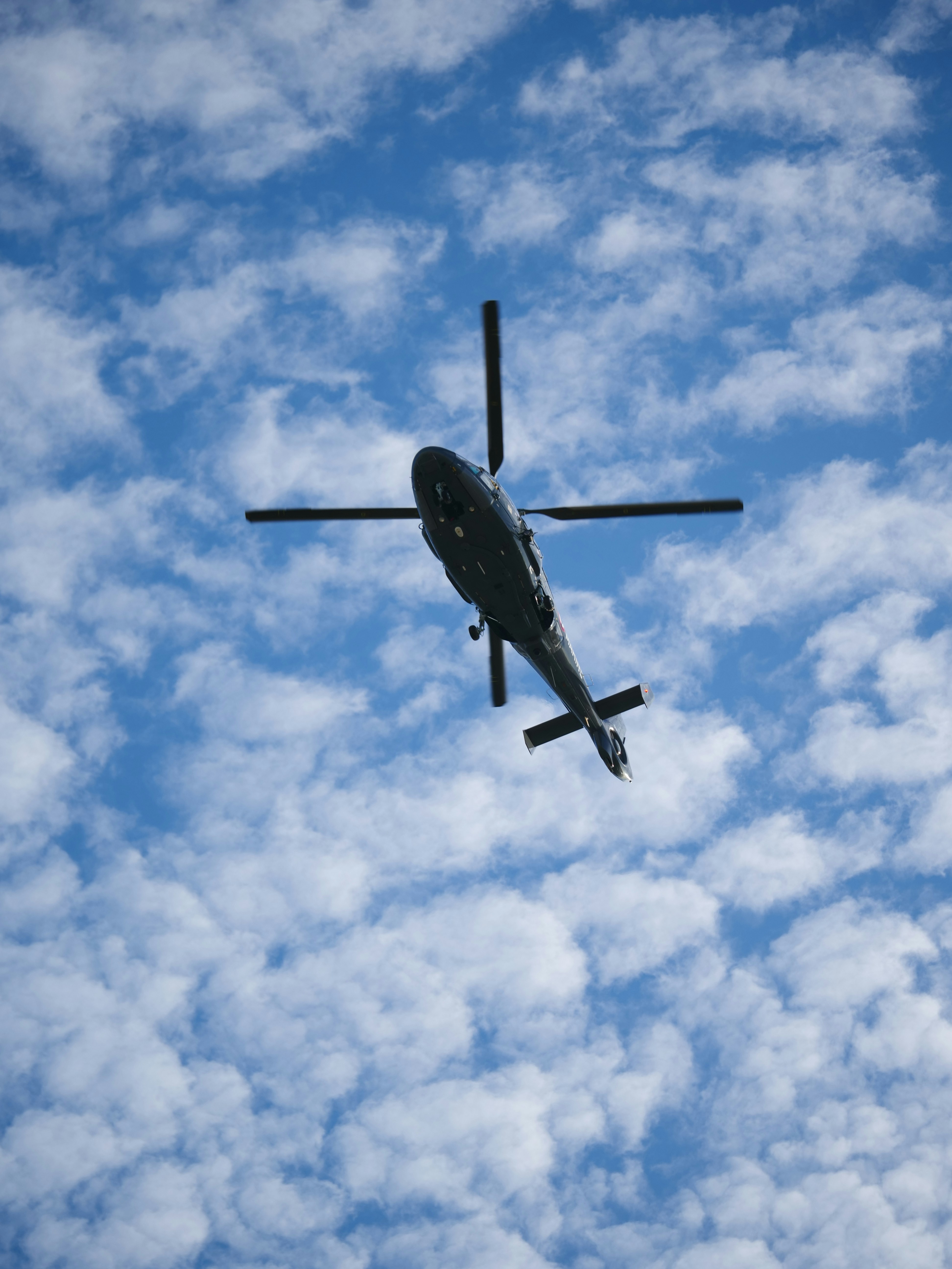 Midair silhouette: a black helicopter gliding through a quilted blue sky
